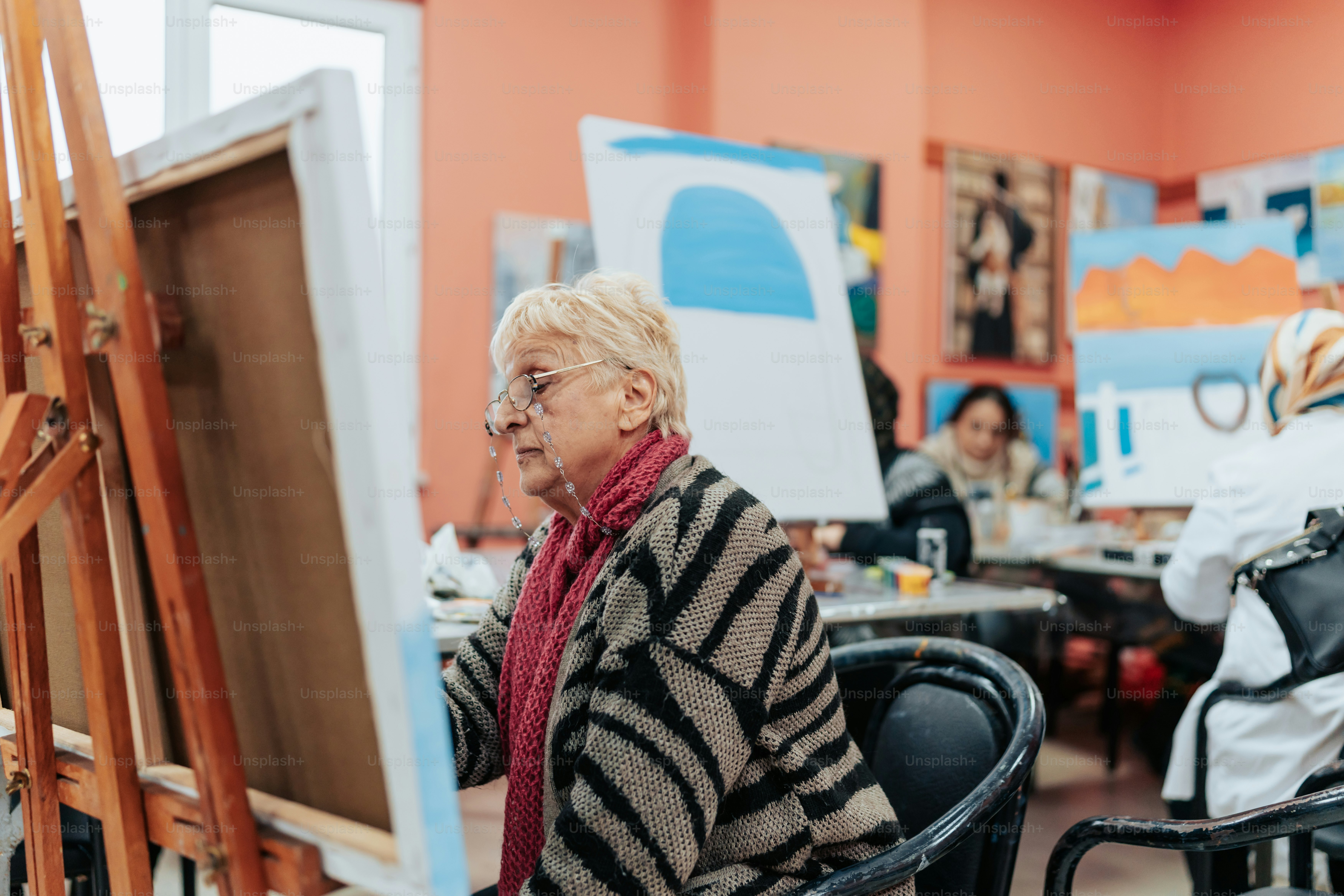 A woman sitting in front of a easel painting photo – Art class Image on ...