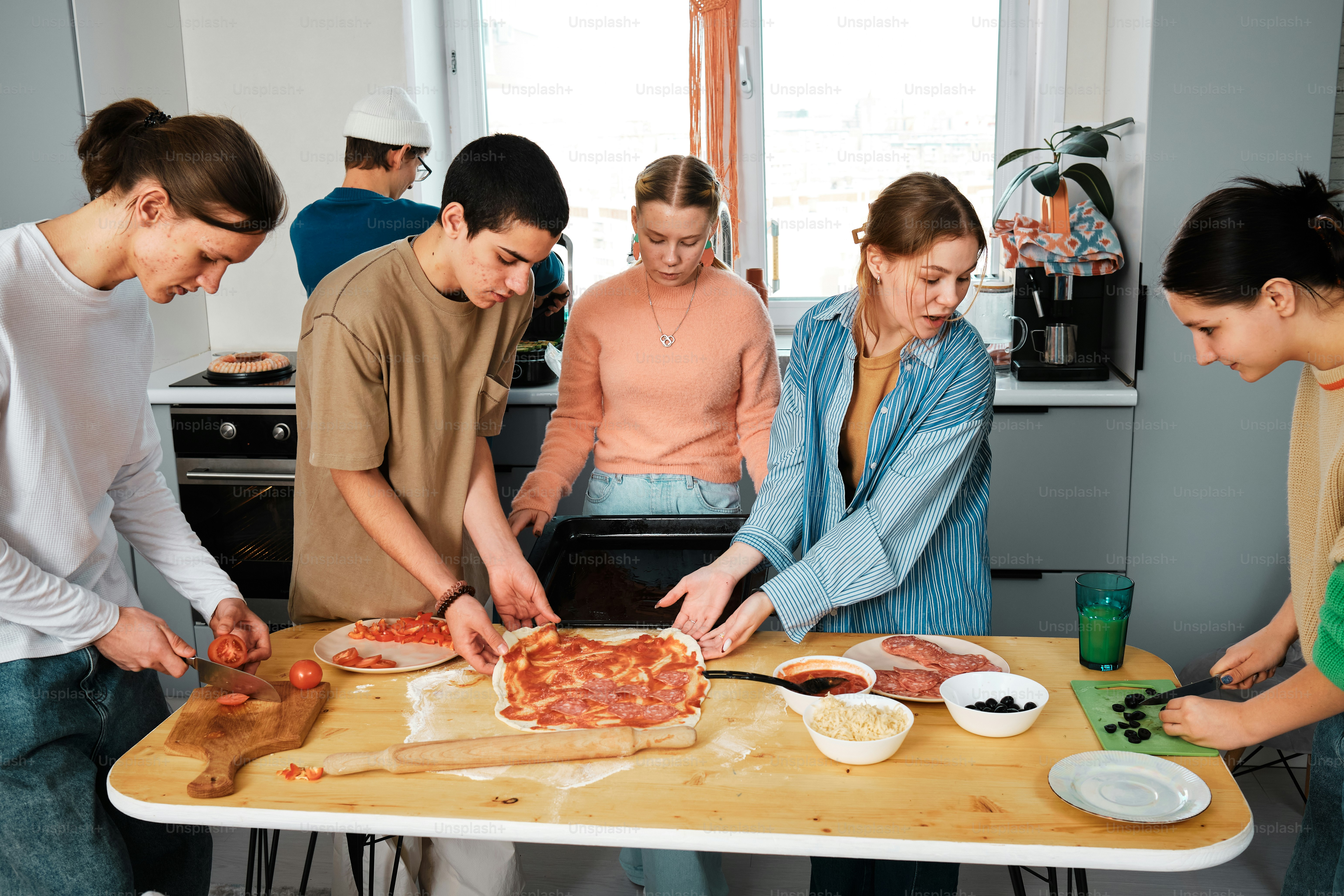 A group of people standing around a table preparing food photo ...
