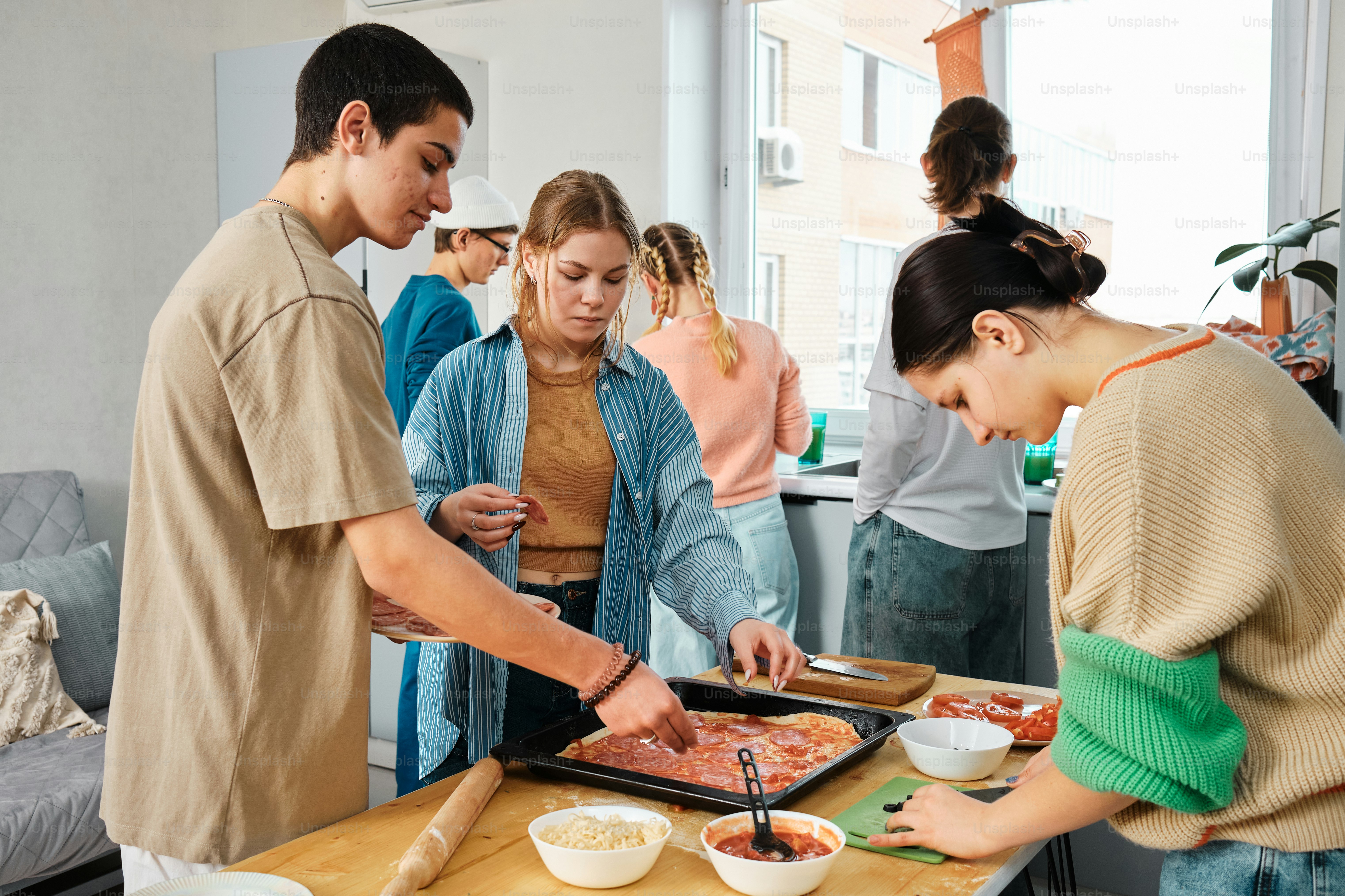 A group of people standing around a table preparing food photo ...