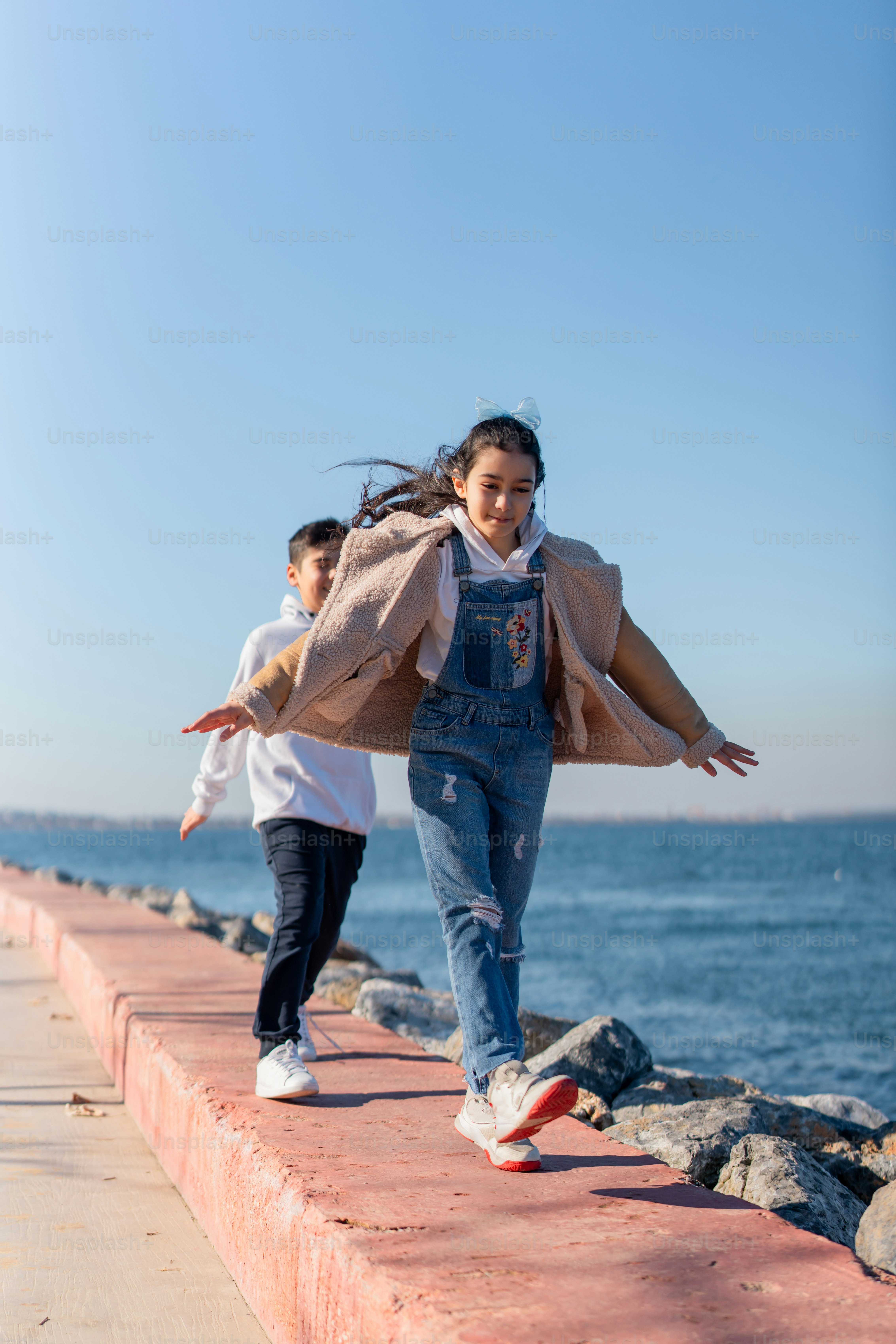 Two young girls are running along a brick wall by the water photo ...