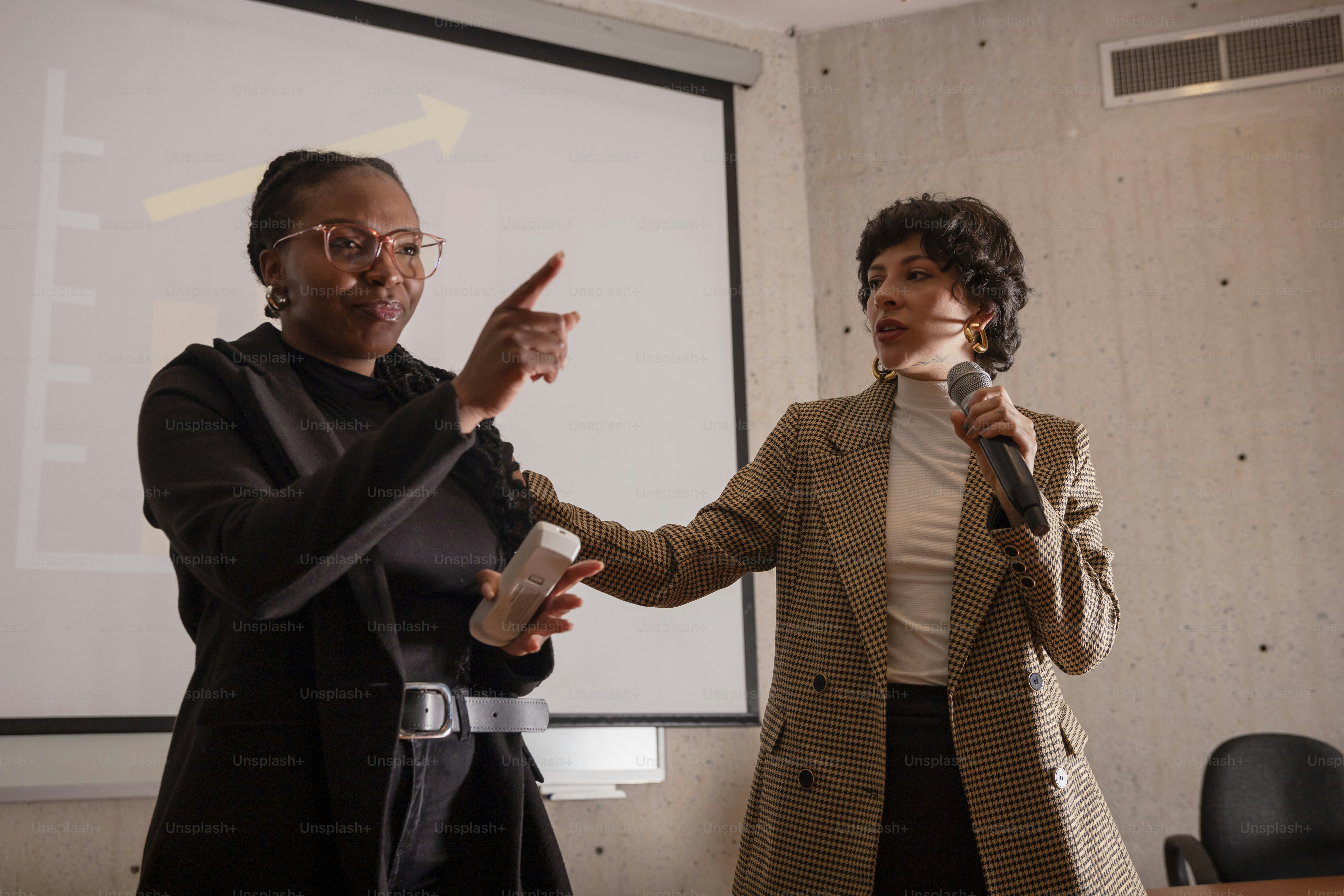 Two women standing next to each other in front of a projector screen ...