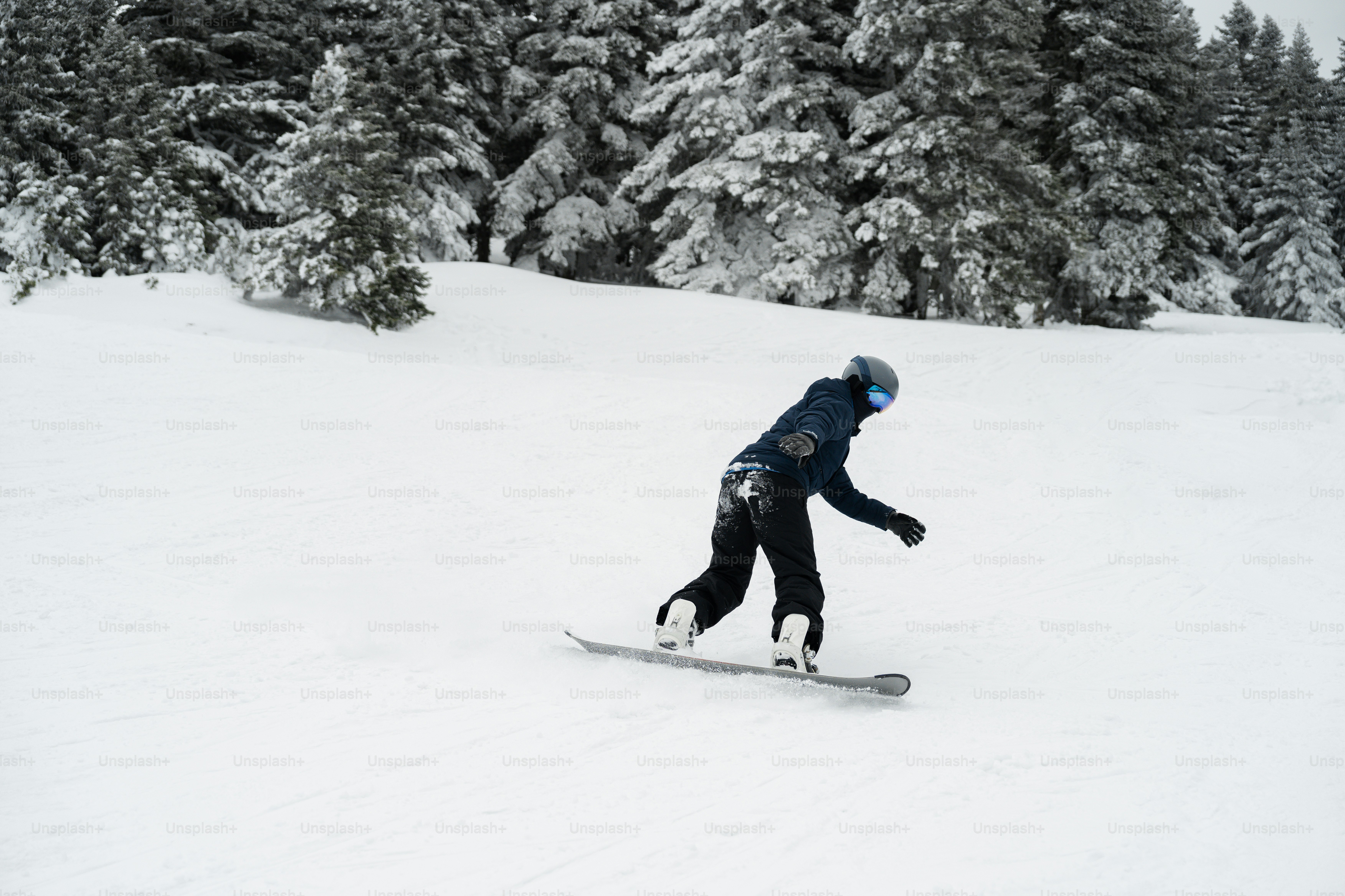A man riding a snowboard down a snow covered slope photo – Snowboarding ...