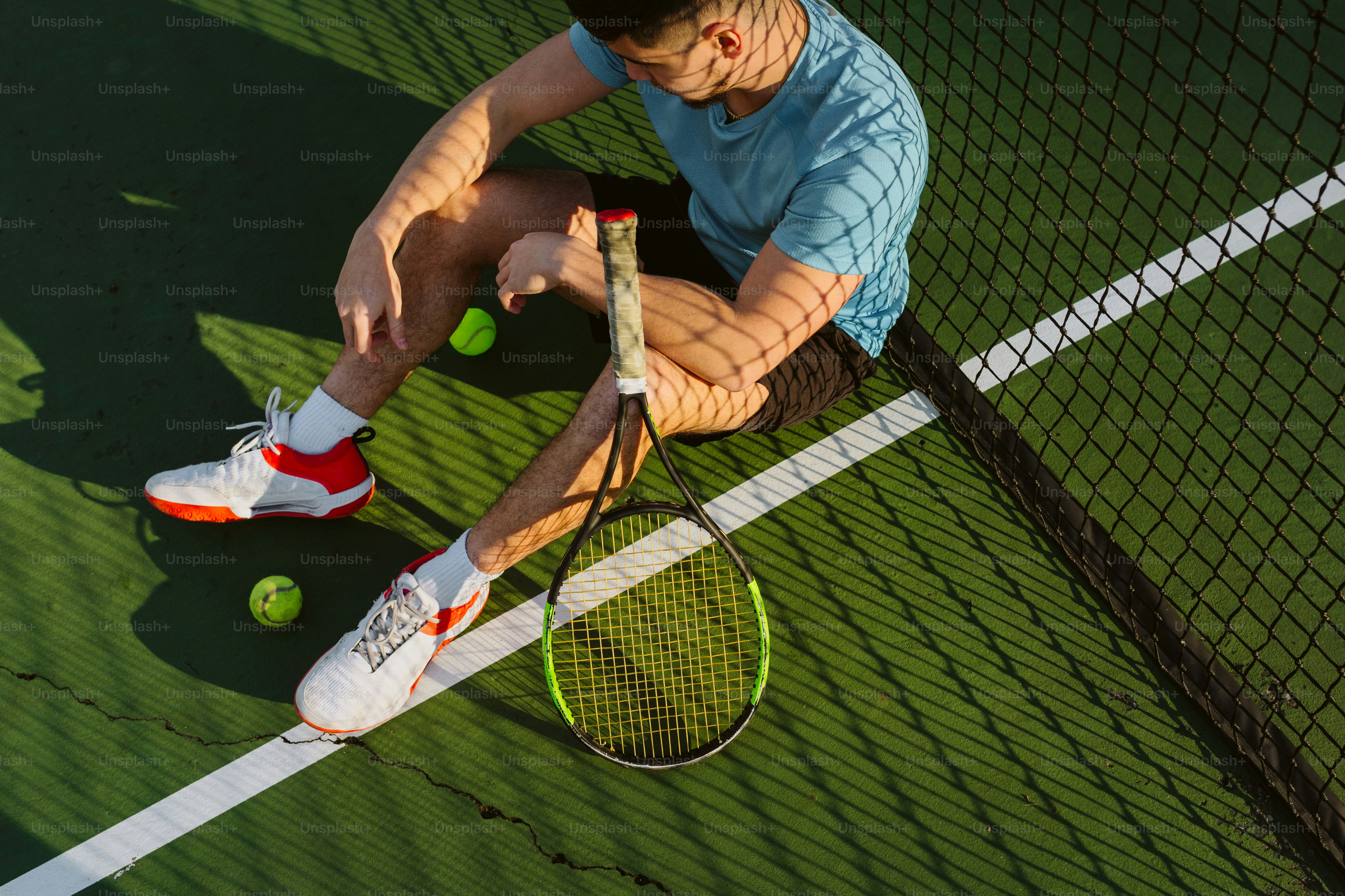 A man sitting on a tennis court holding a racquet photo – Tennis ball ...