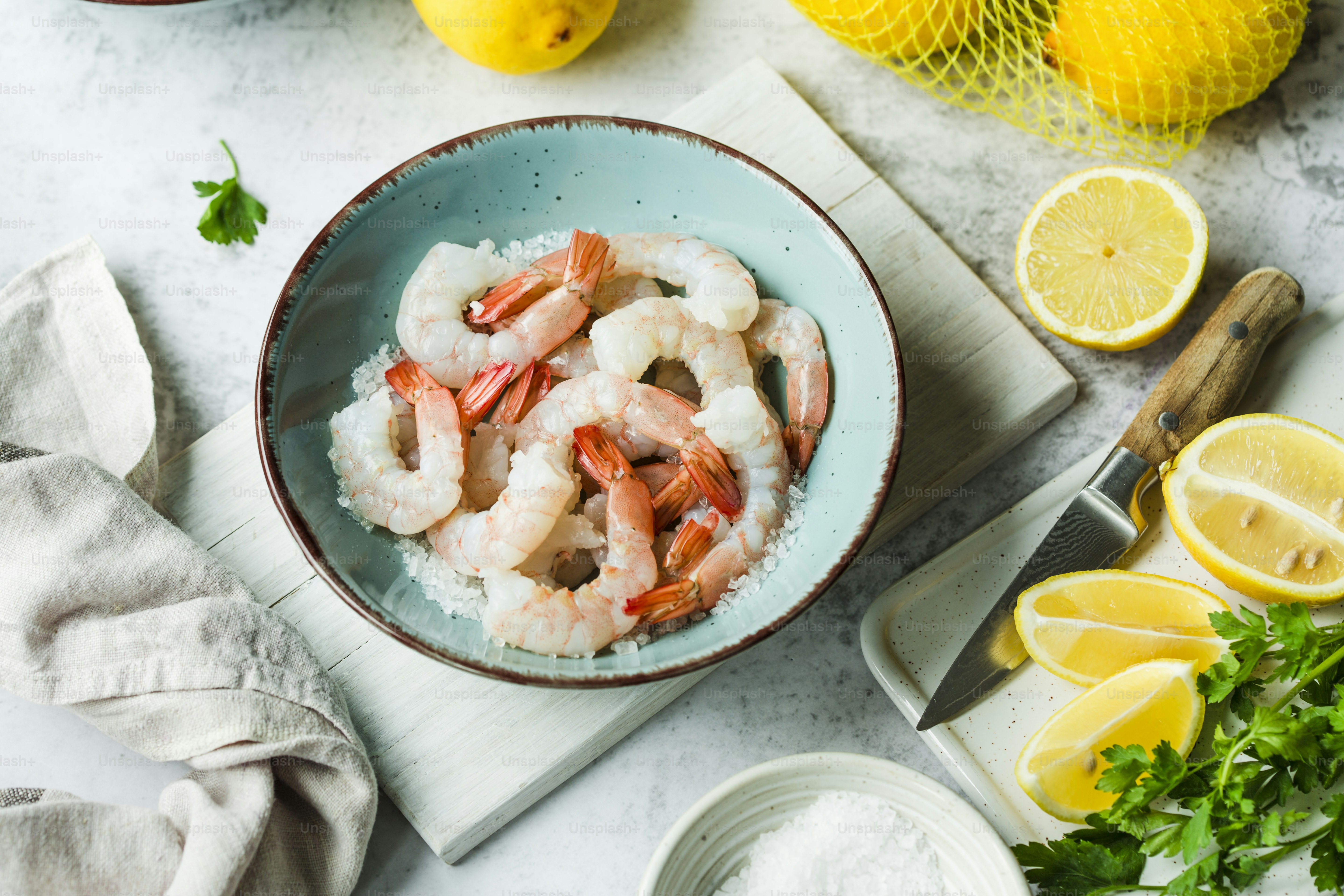 A bowl filled with shrimp next to lemons and parsley photo – Seafood ...