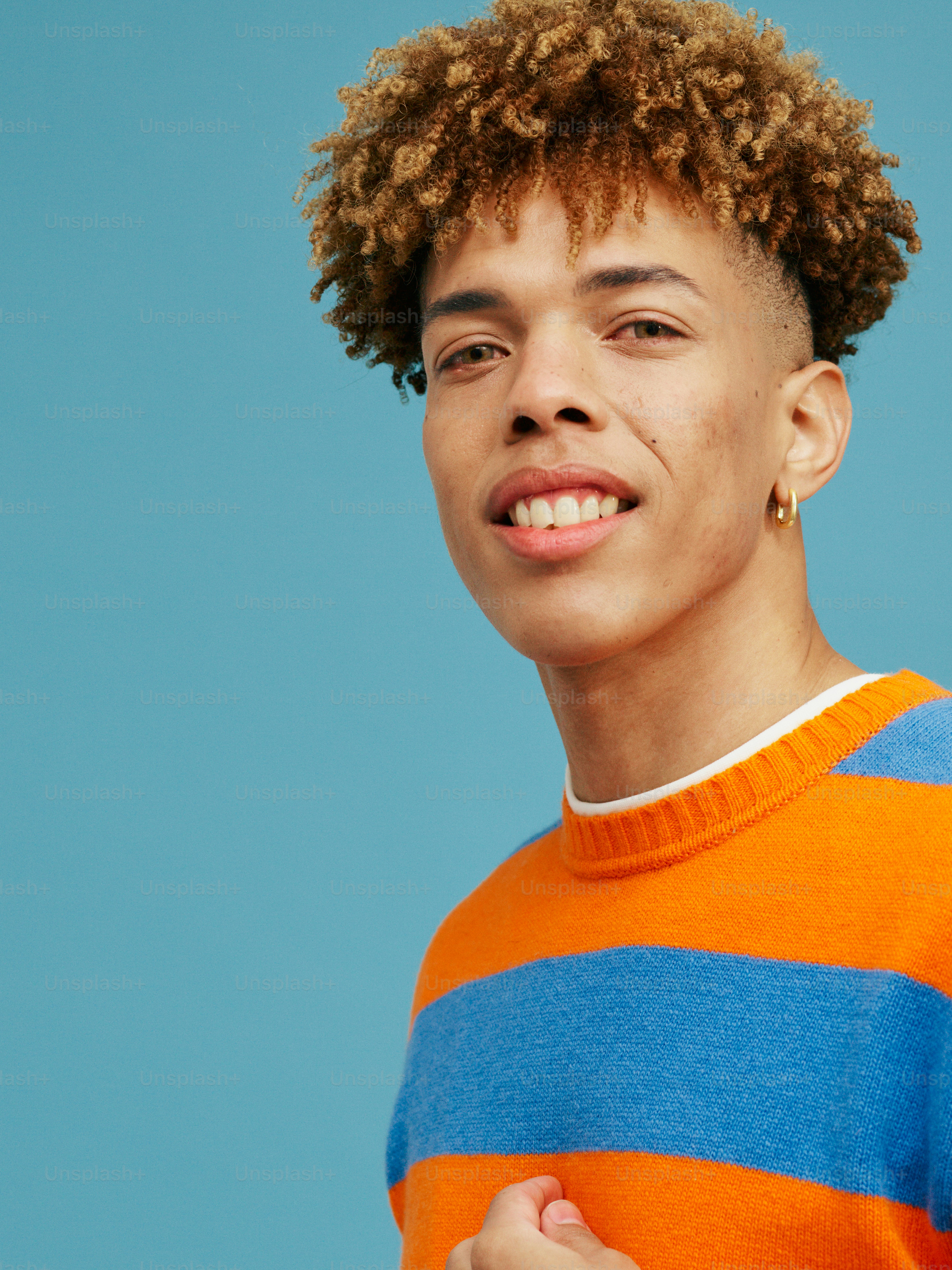 A young man with curly hair wearing an orange, blue, and green jacket ...