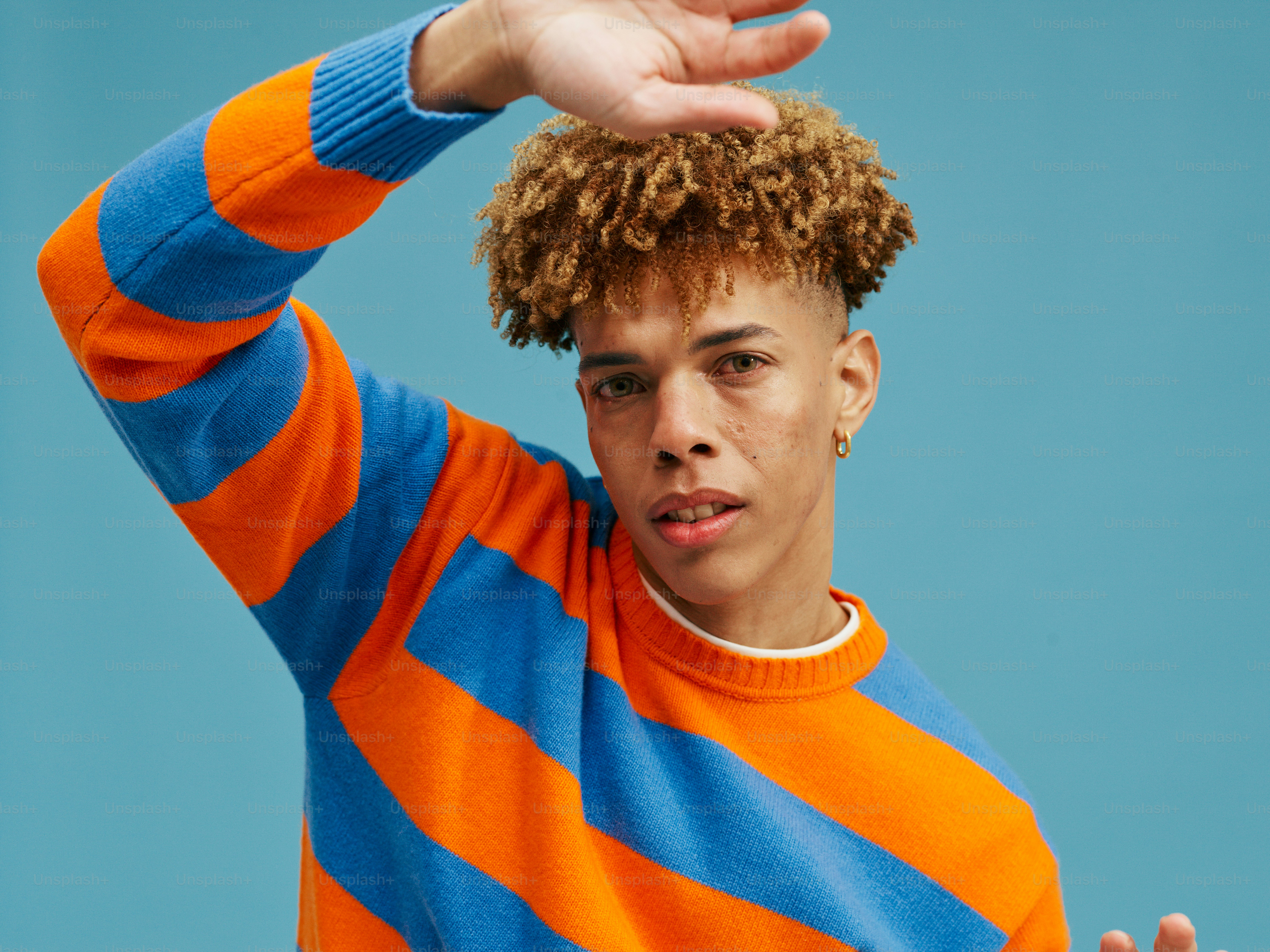 A young man with curly hair wearing an orange, blue, and green jacket ...
