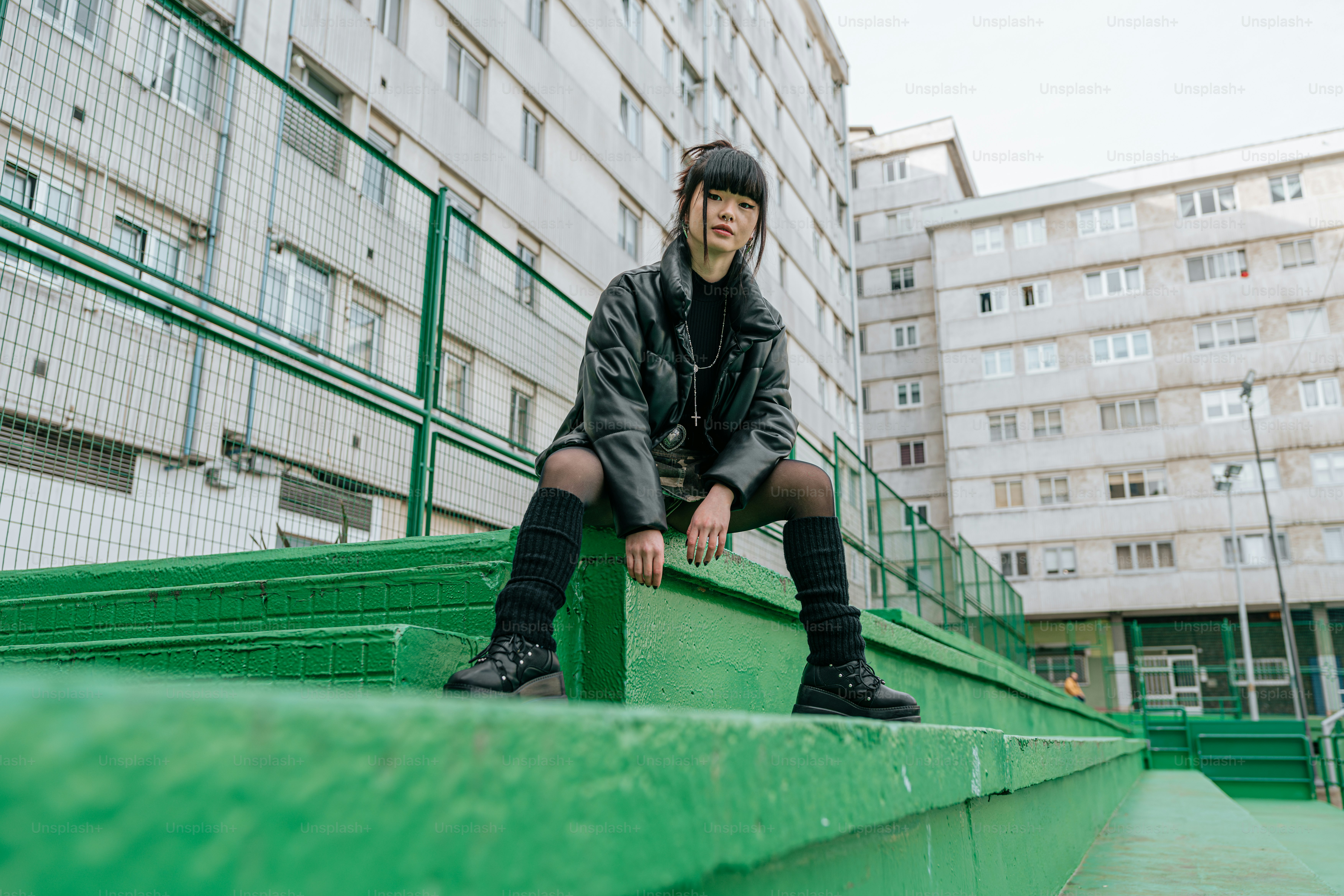 A person sitting on a green rail in front of a building photo – Asian ...