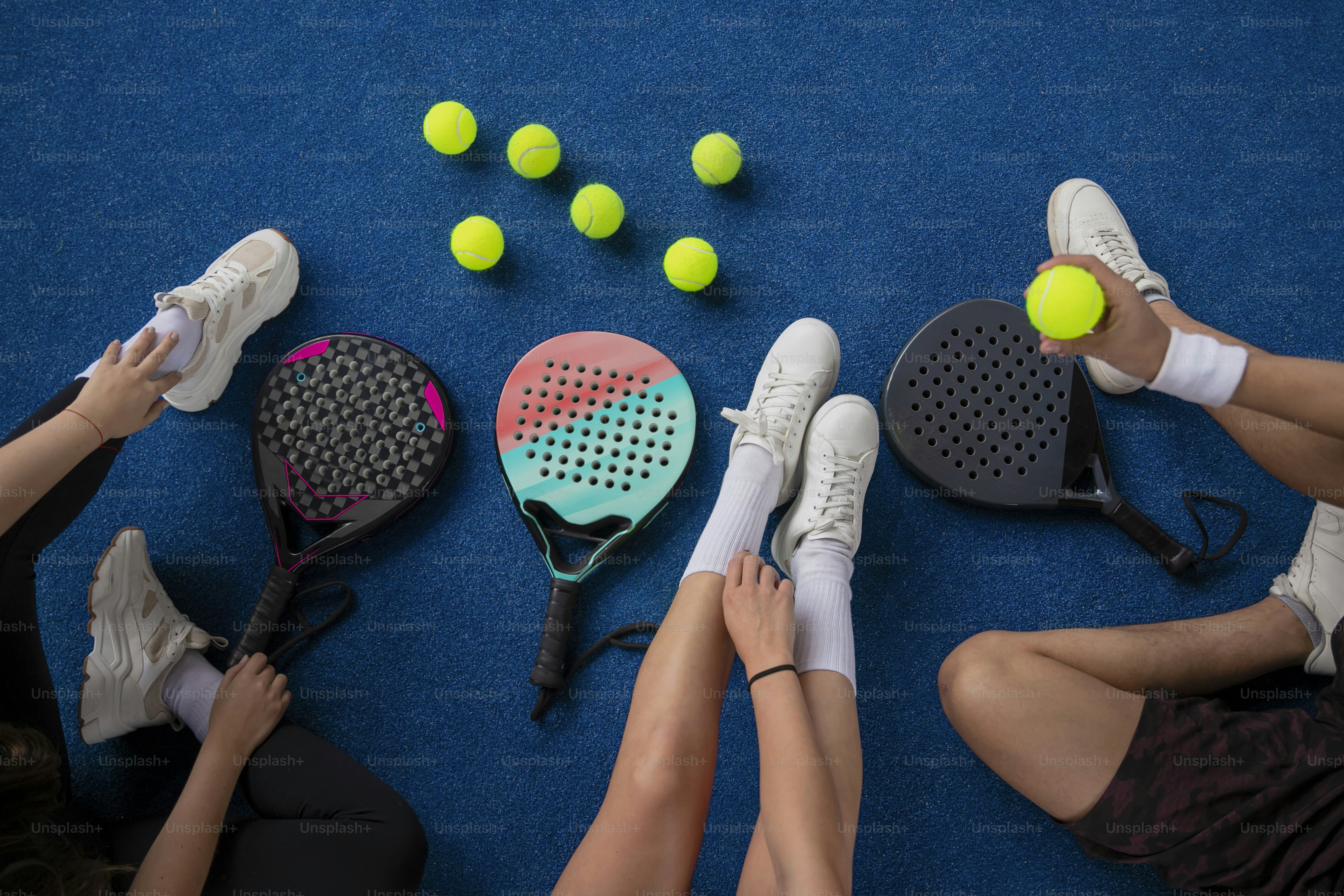 A group of people sitting on the ground with tennis rackets and balls ...