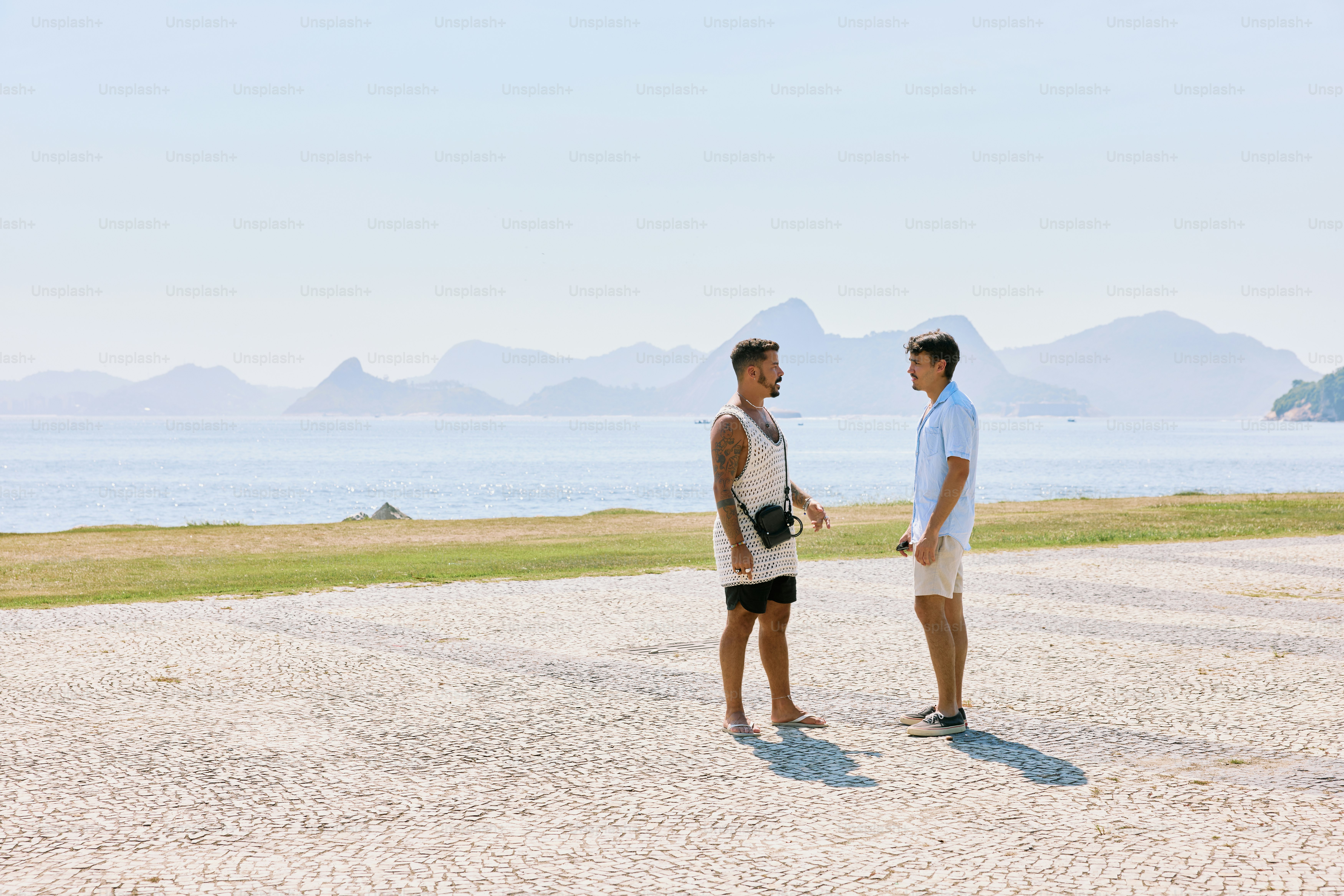 A couple of men standing on top of a sandy beach photo – Gay men Image ...
