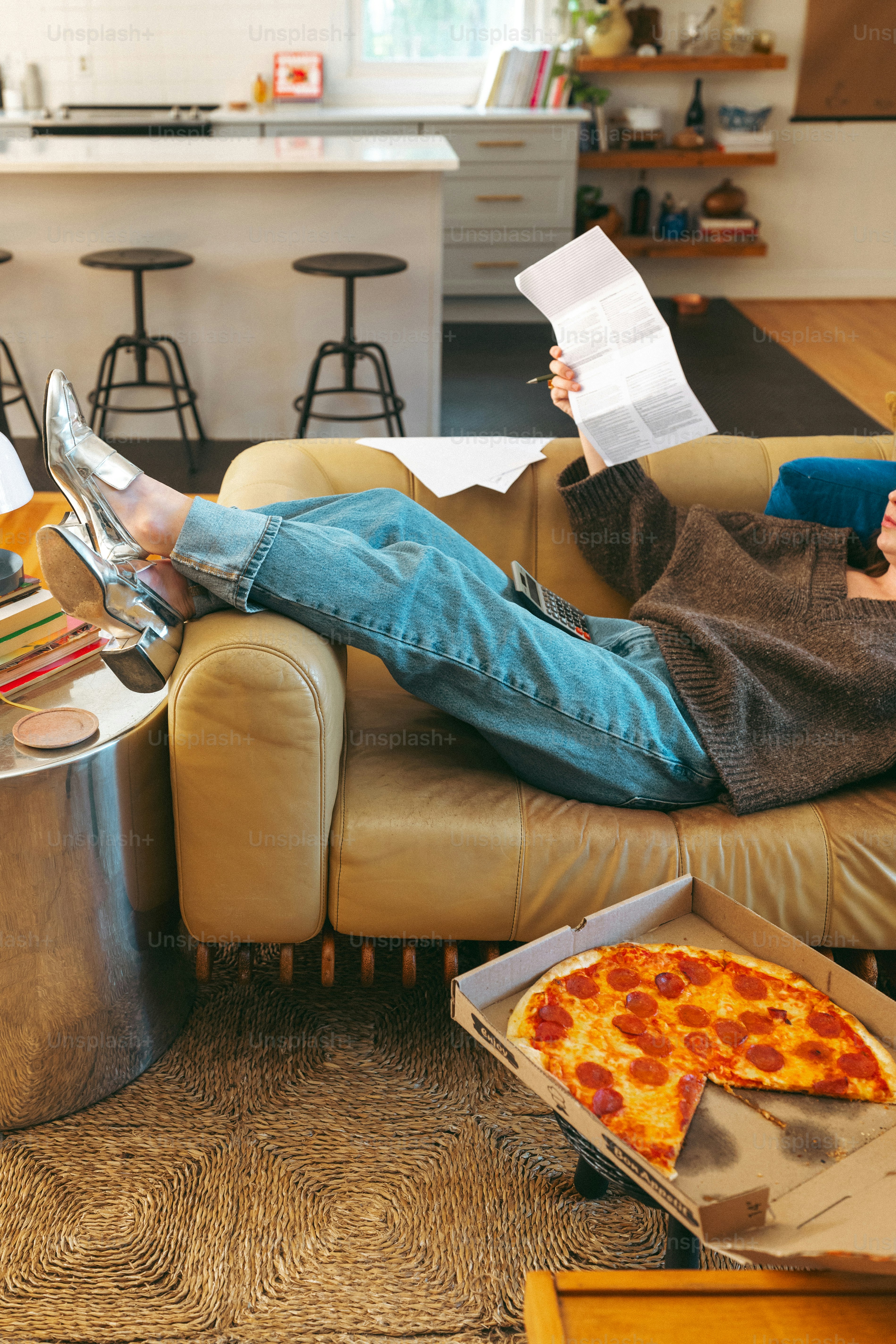 A person sitting on a couch reading a book and eating pizza photo ...