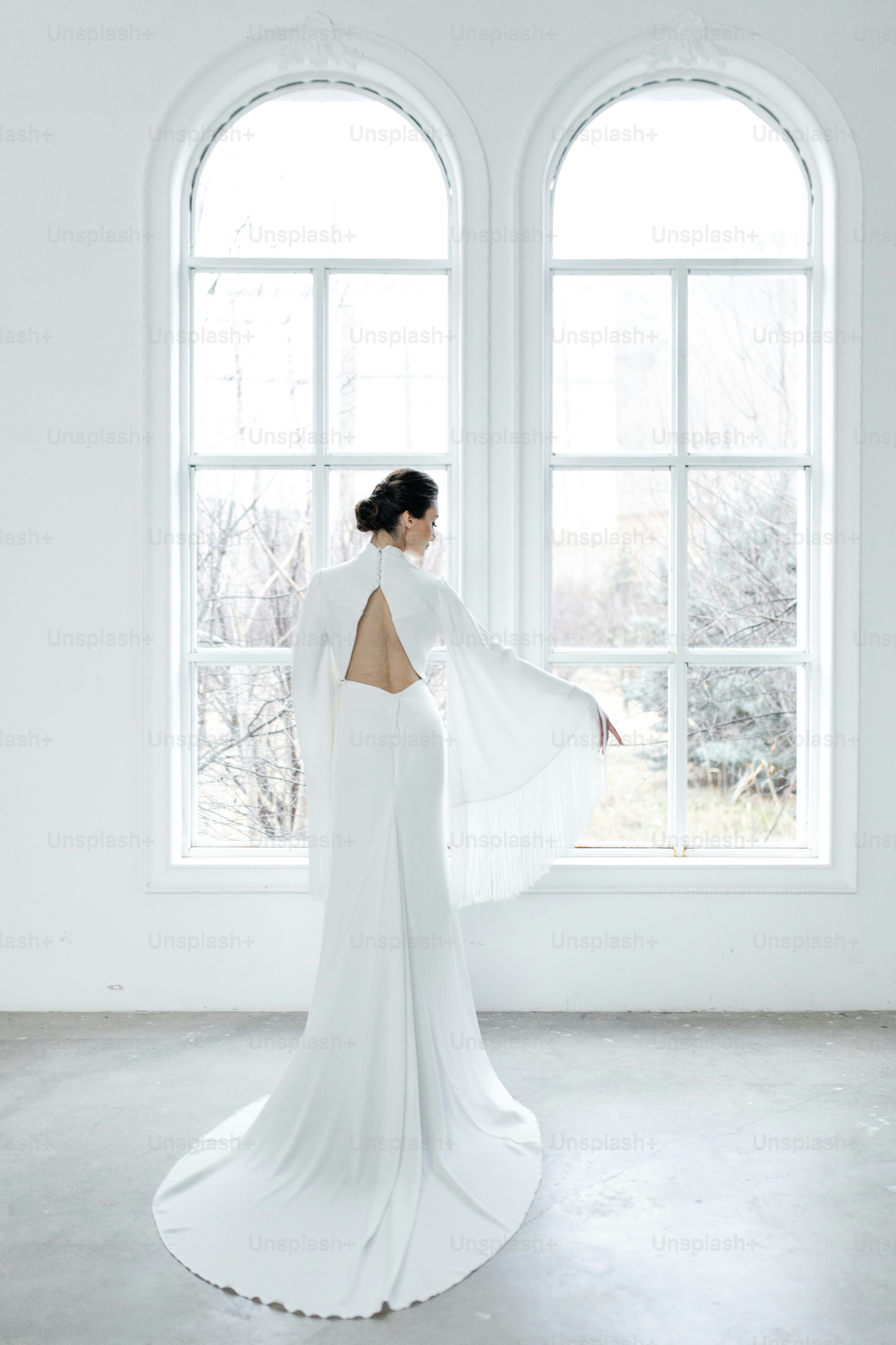 A woman in a white dress standing in front of a window photo – White ...