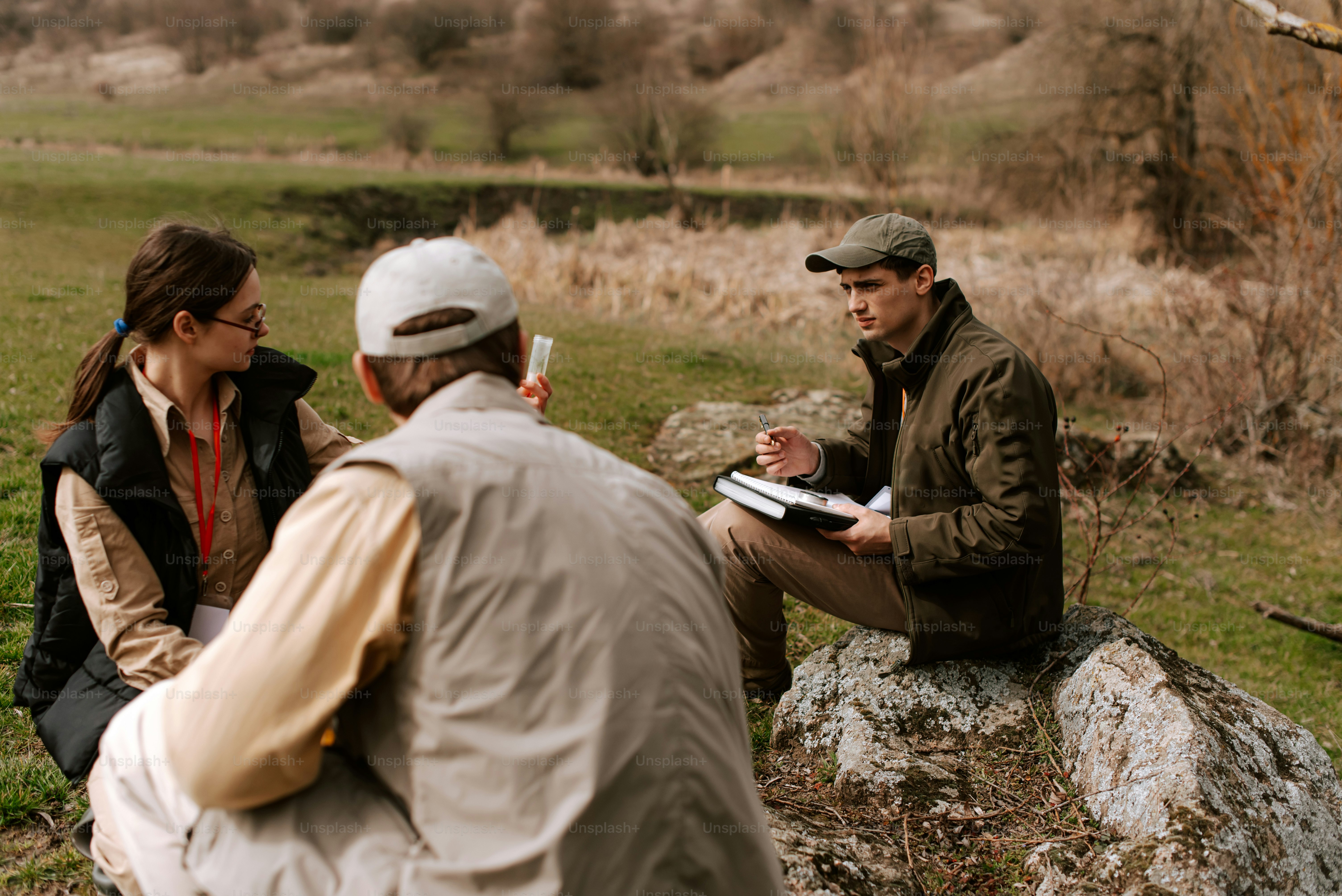 A group of people sitting on a rock in a field photo – Nature Image on ...