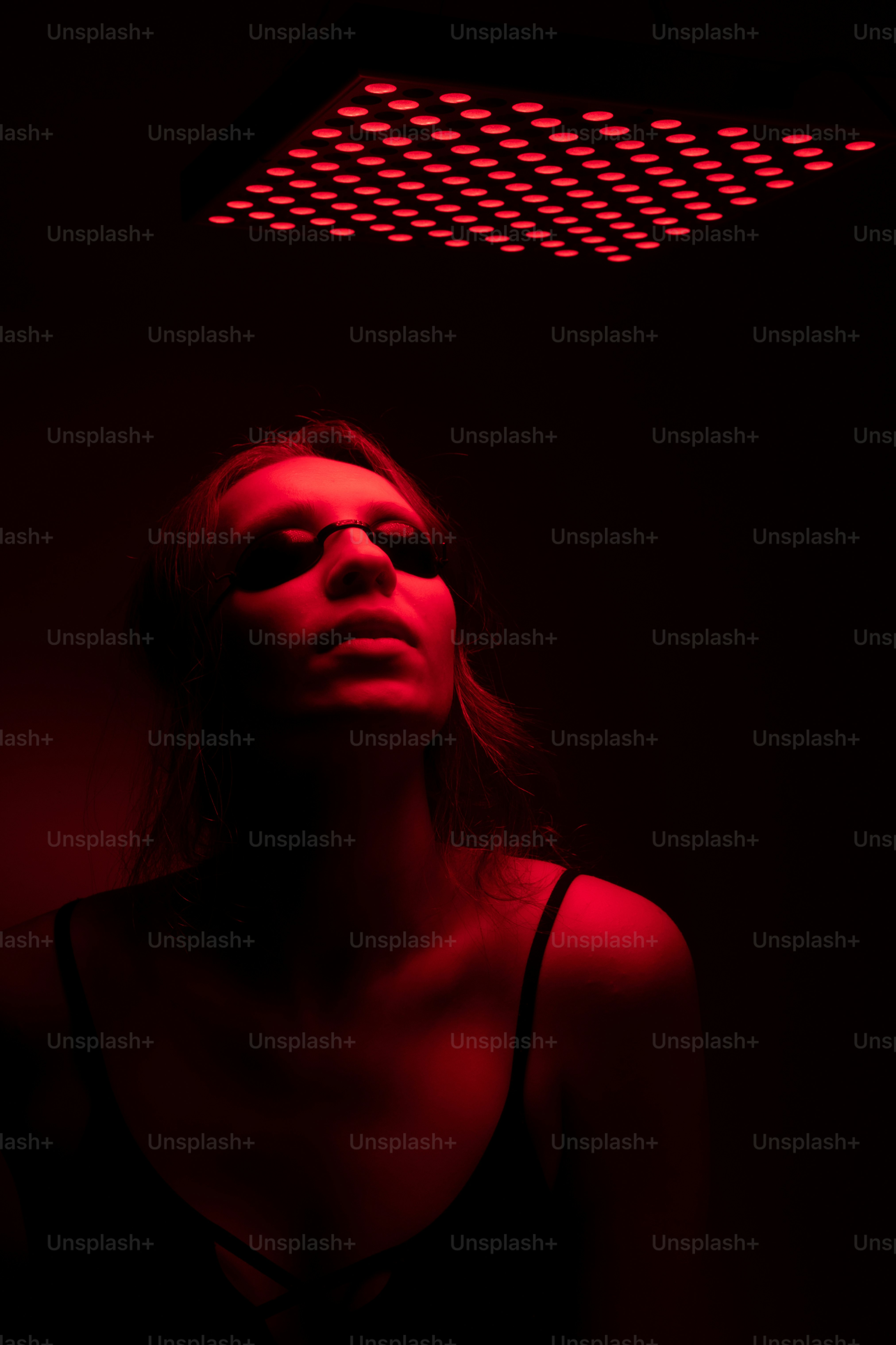 A woman in a dark room with a red light photo – Red light therapy Image ...