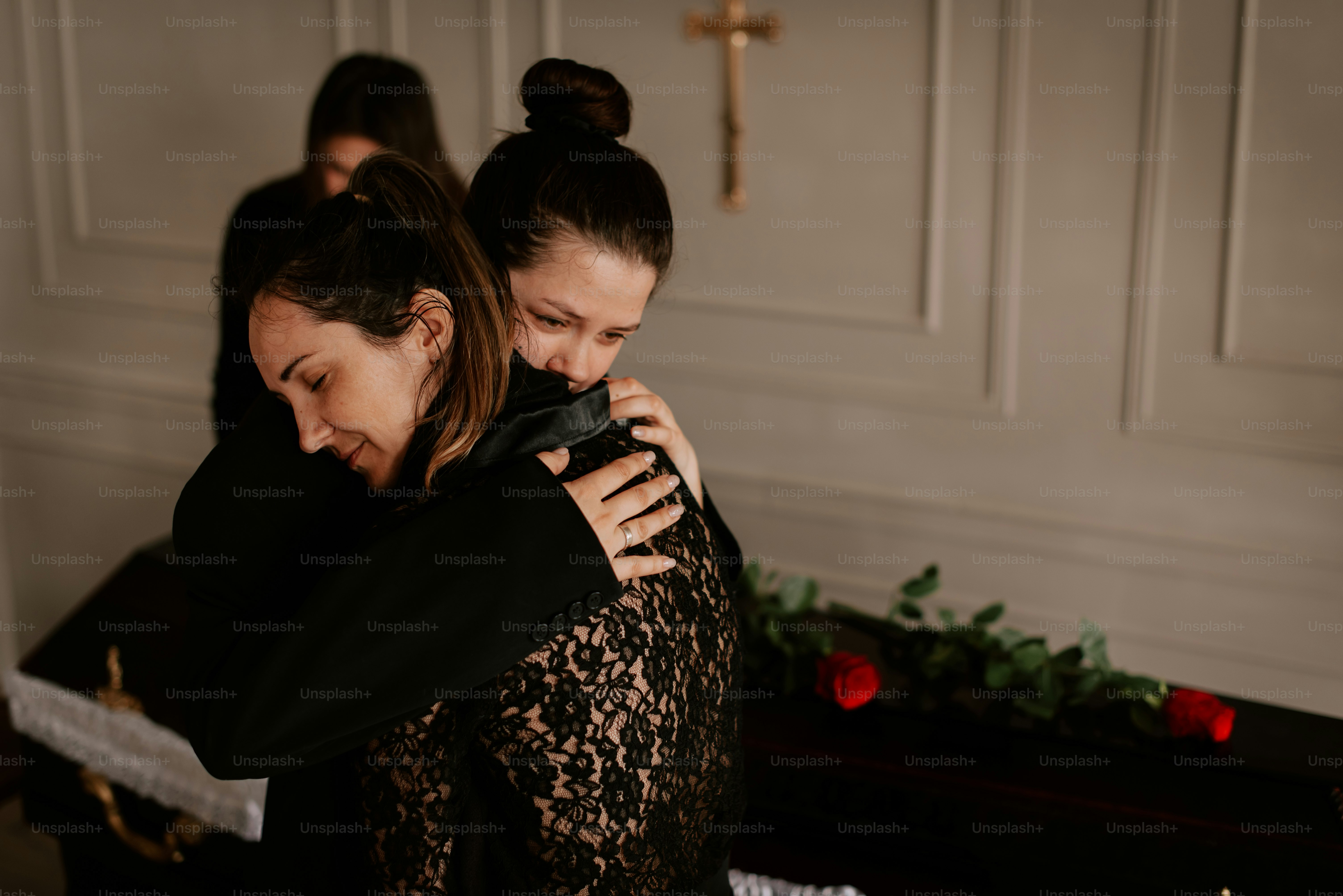 Two women hugging each other in front of a cross photo – Funeral ...