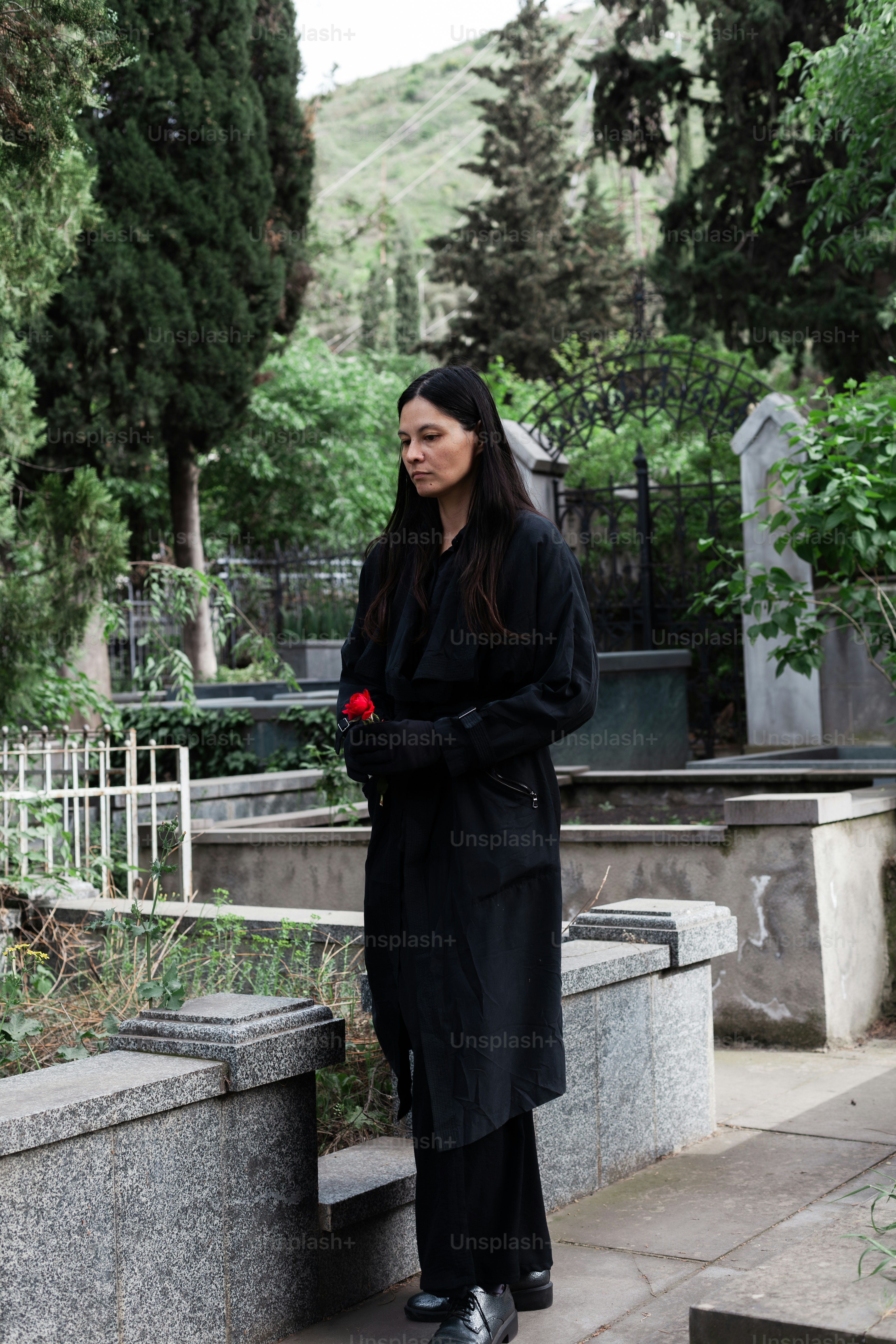 A woman in a long black coat standing on a stone bench photo – Death ...