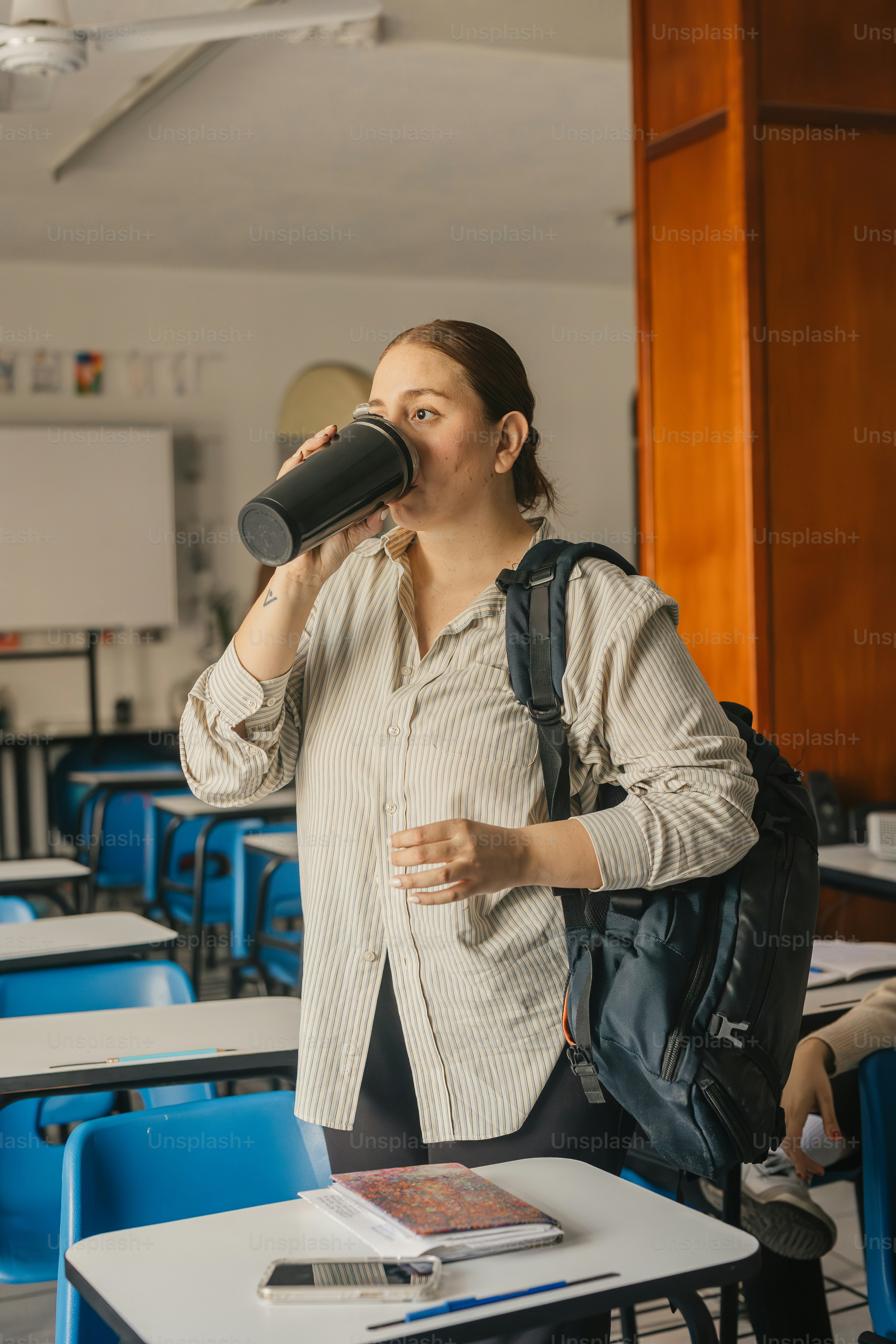 A woman standing in a classroom drinking from a cup photo – Adult ...