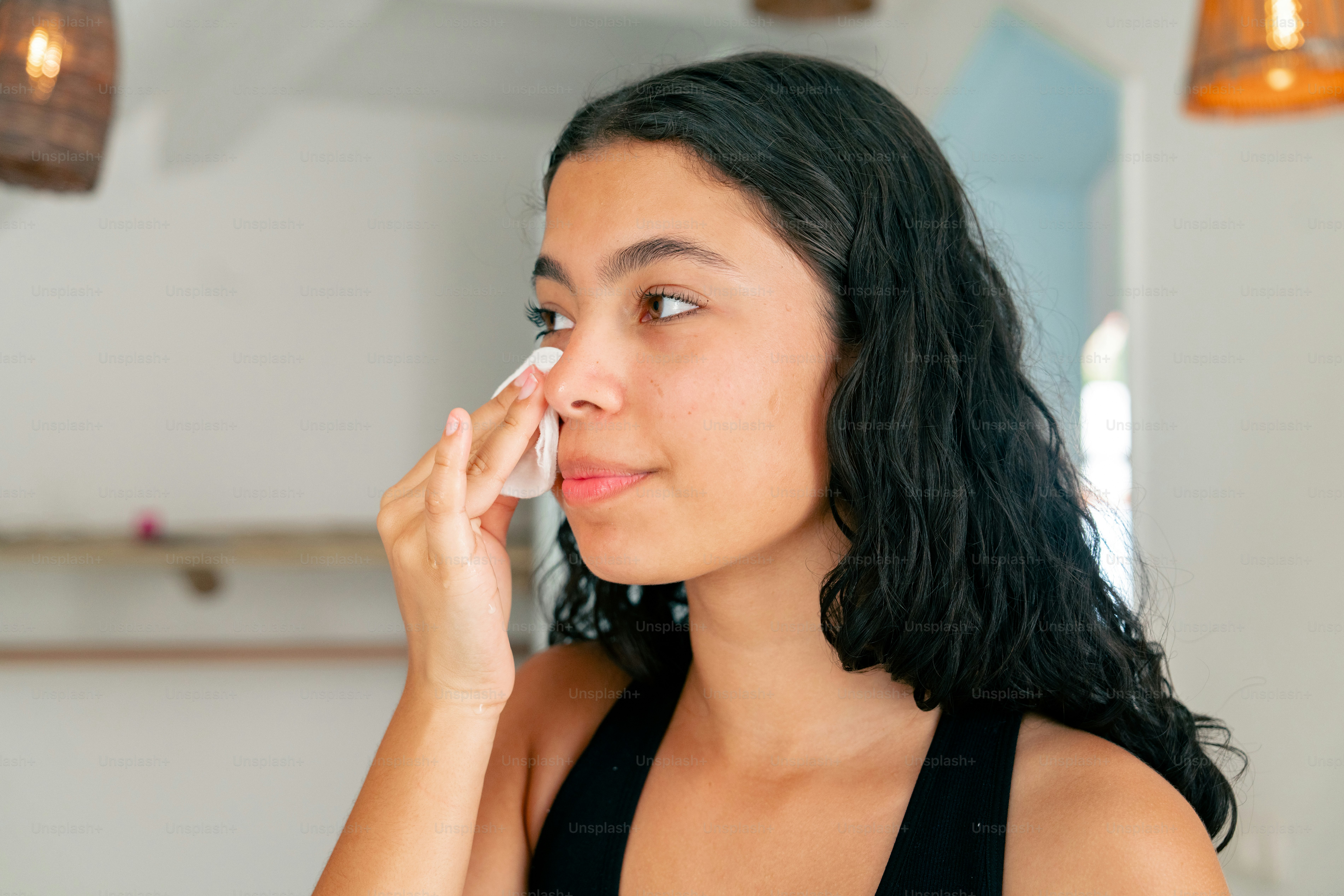 A woman with dark hair and a black tank top is using a cotton swab ...