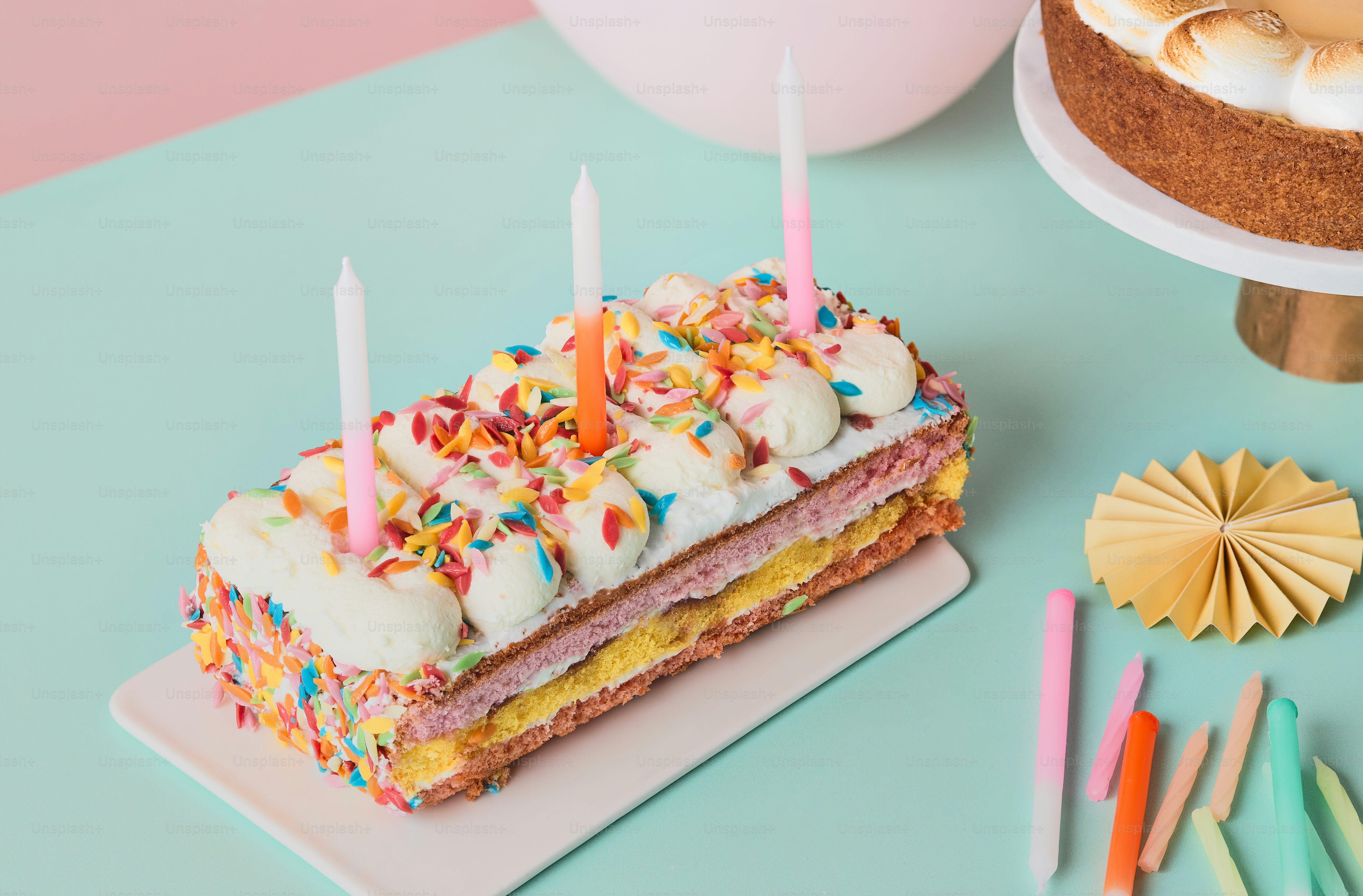 A table topped with cakes and candles next to a pink wall photo ...