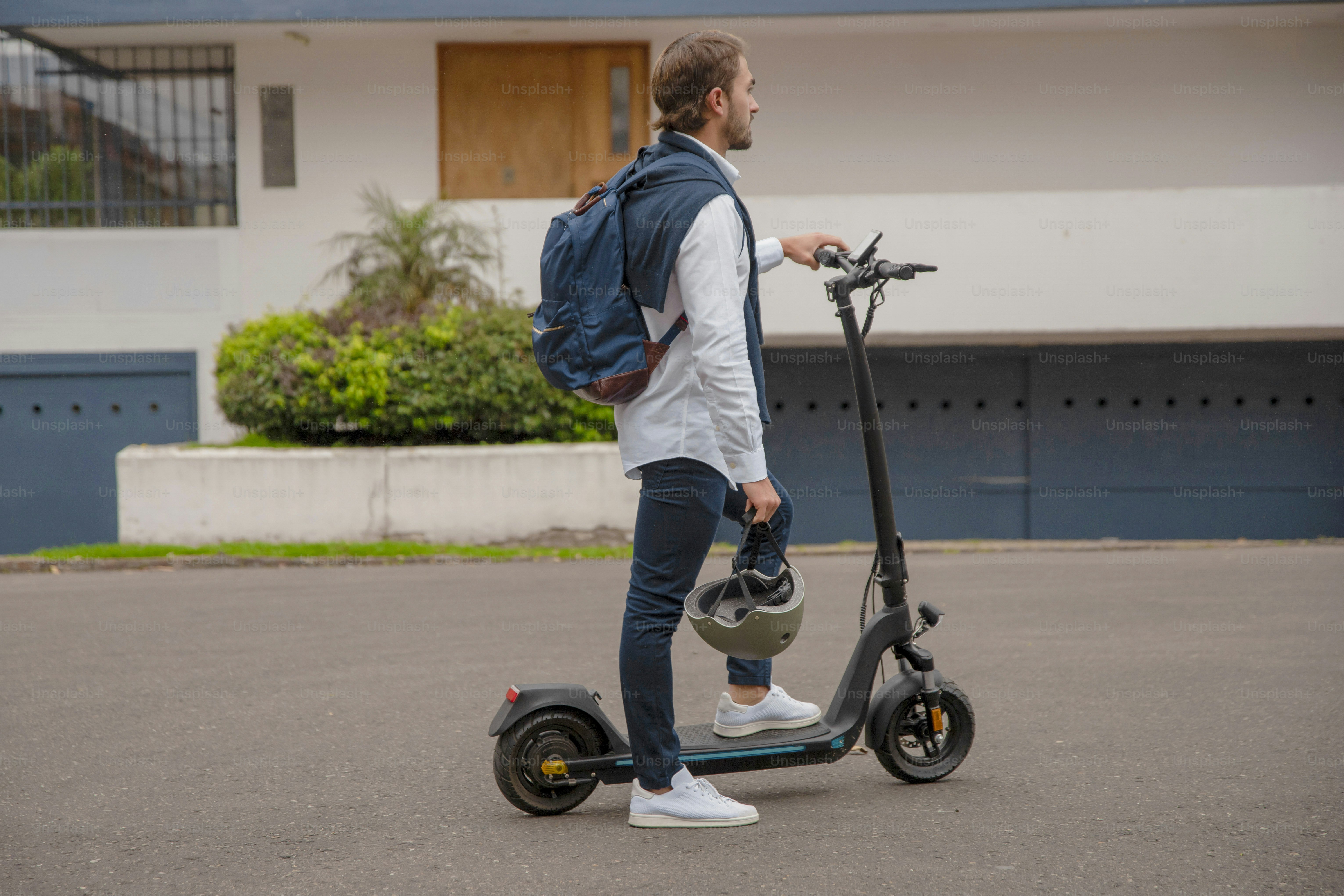 A man riding a scooter with a backpack on it photo – Sustainability ...