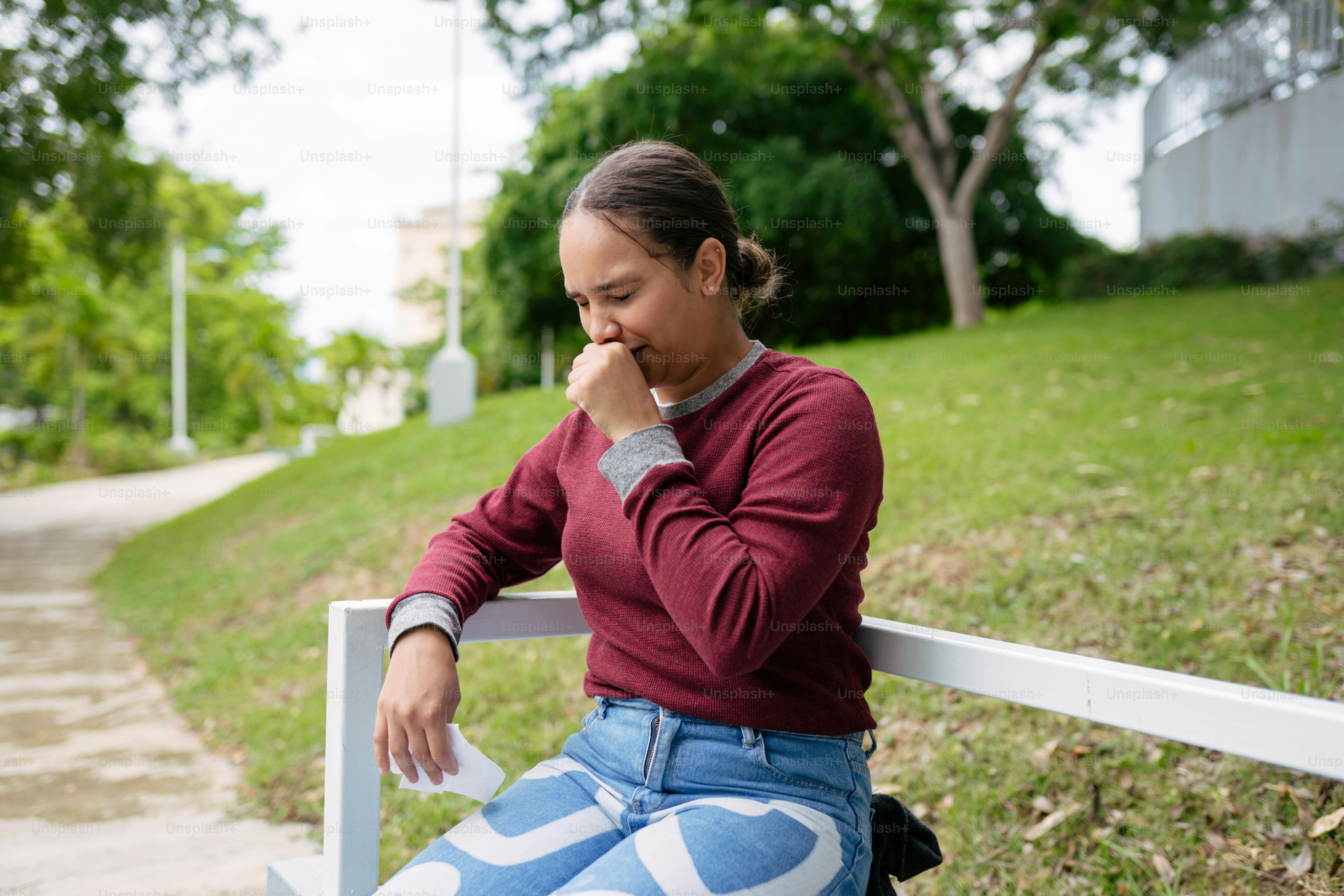 A woman sitting on a bench with her hand to her mouth photo – Hay fever ...