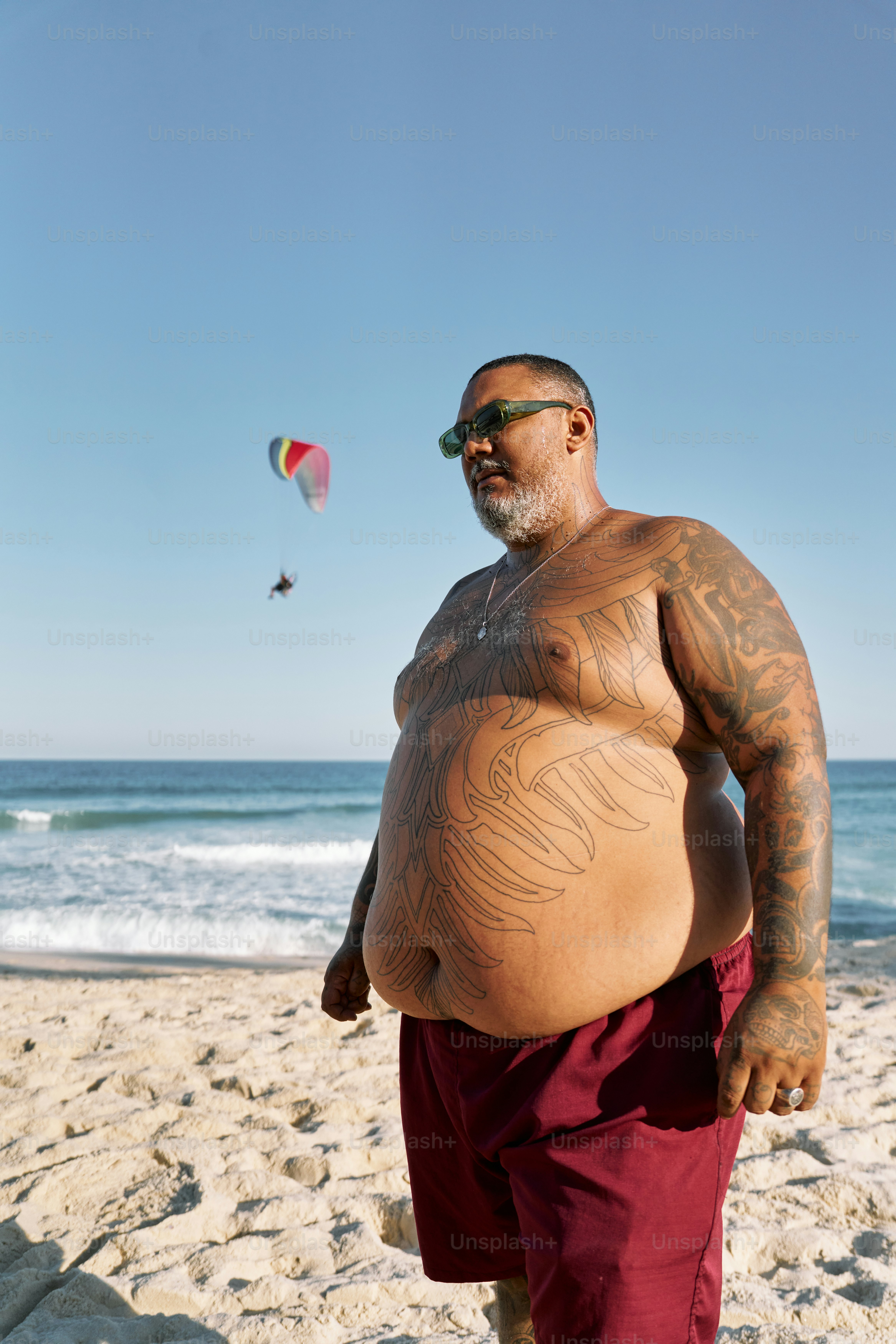 A fat man on the beach with a kite in the background photo – Surfer ...