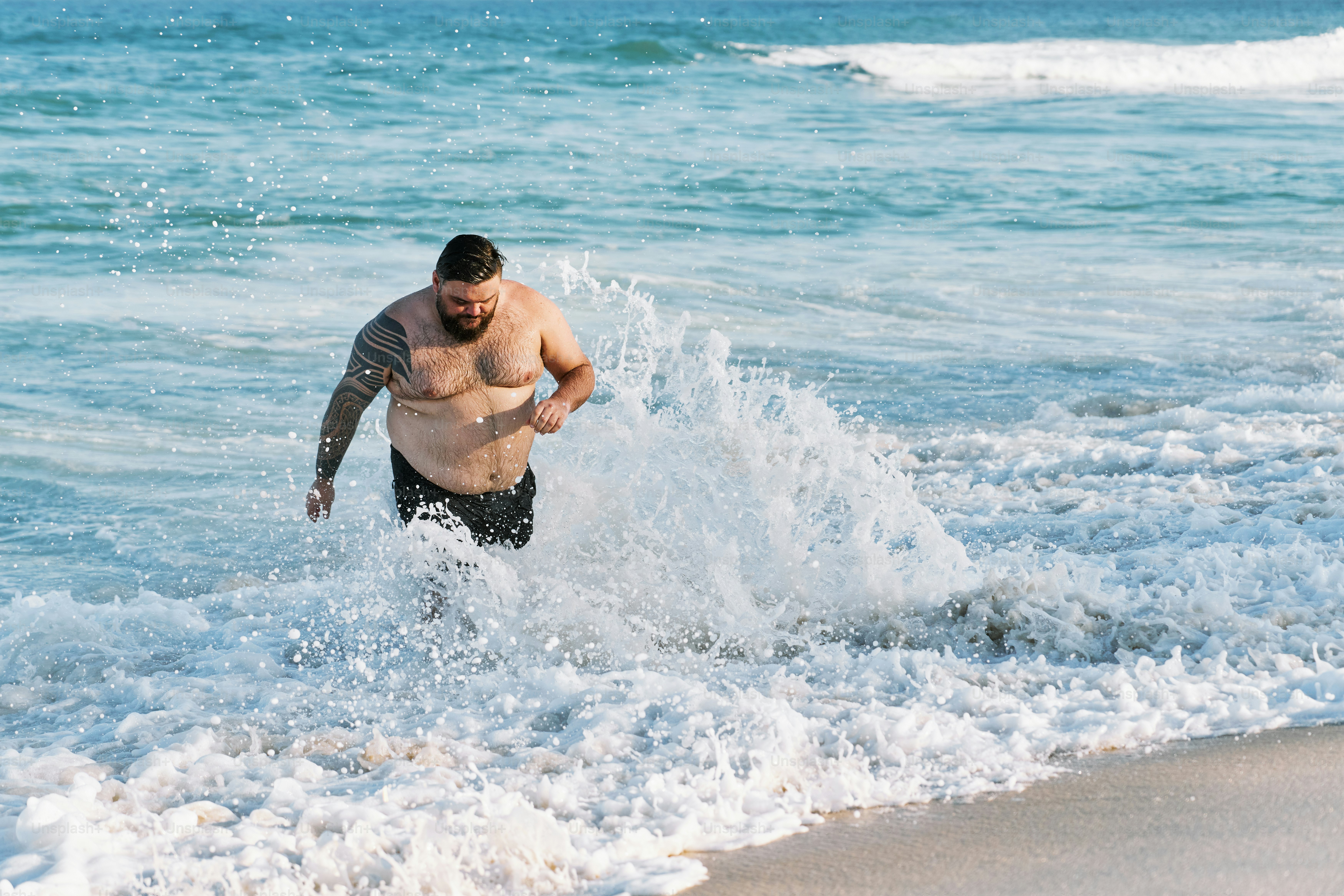 A man running out of the water at the beach photo – Body positivity ...