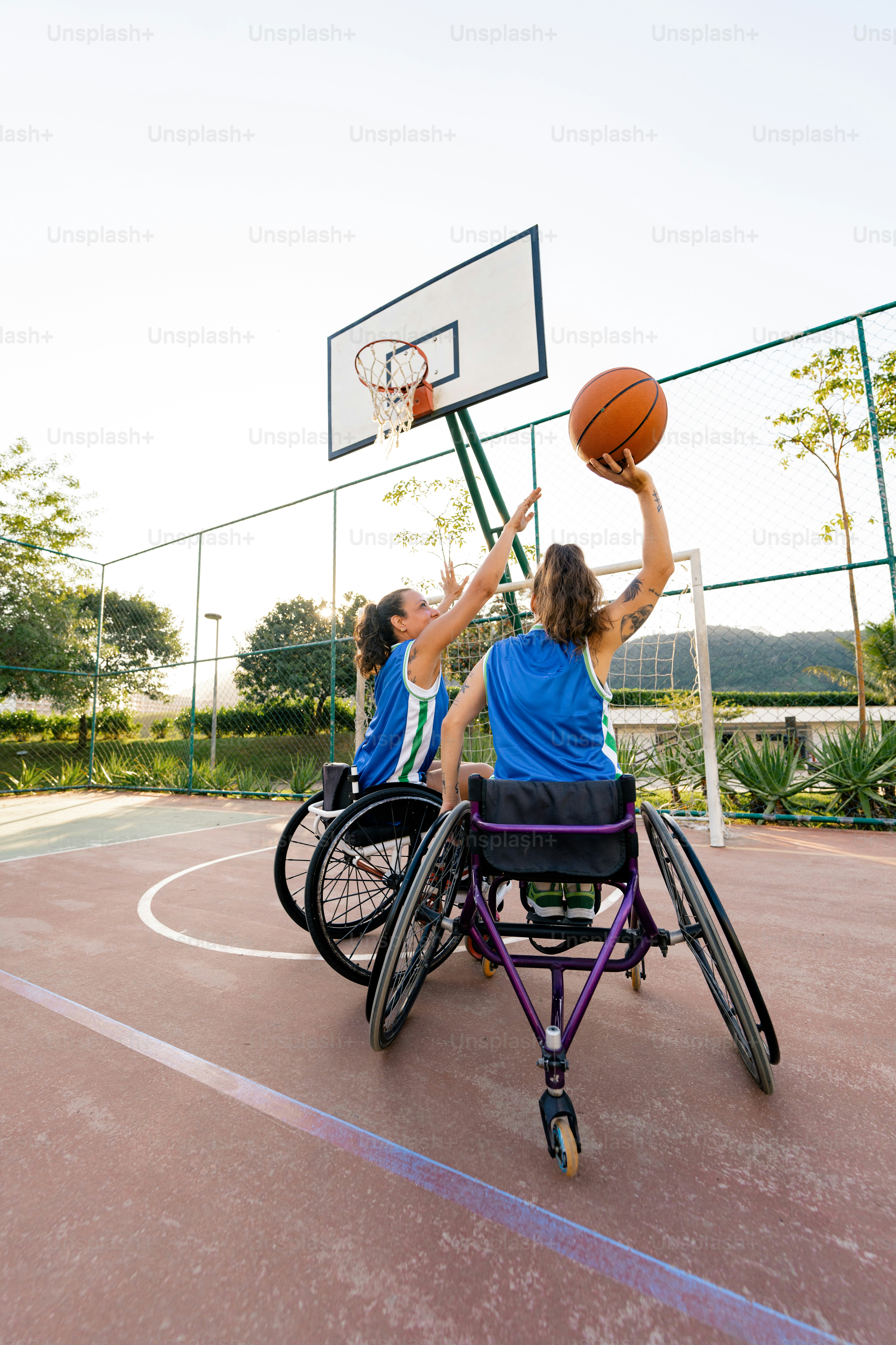 Two people in wheelchairs playing basketball on a court photo ...
