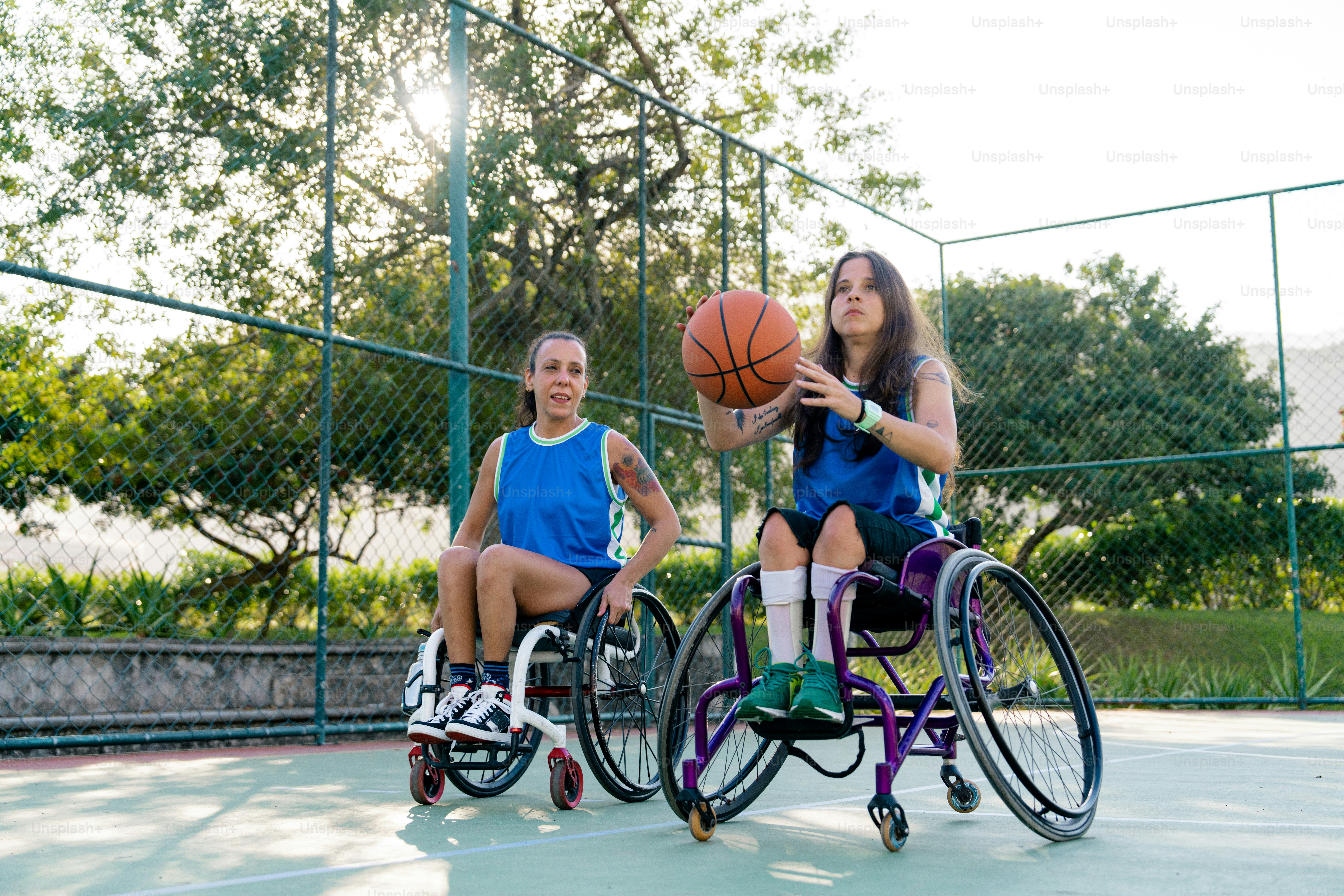 Two women in wheelchairs playing basketball on a court photo ...