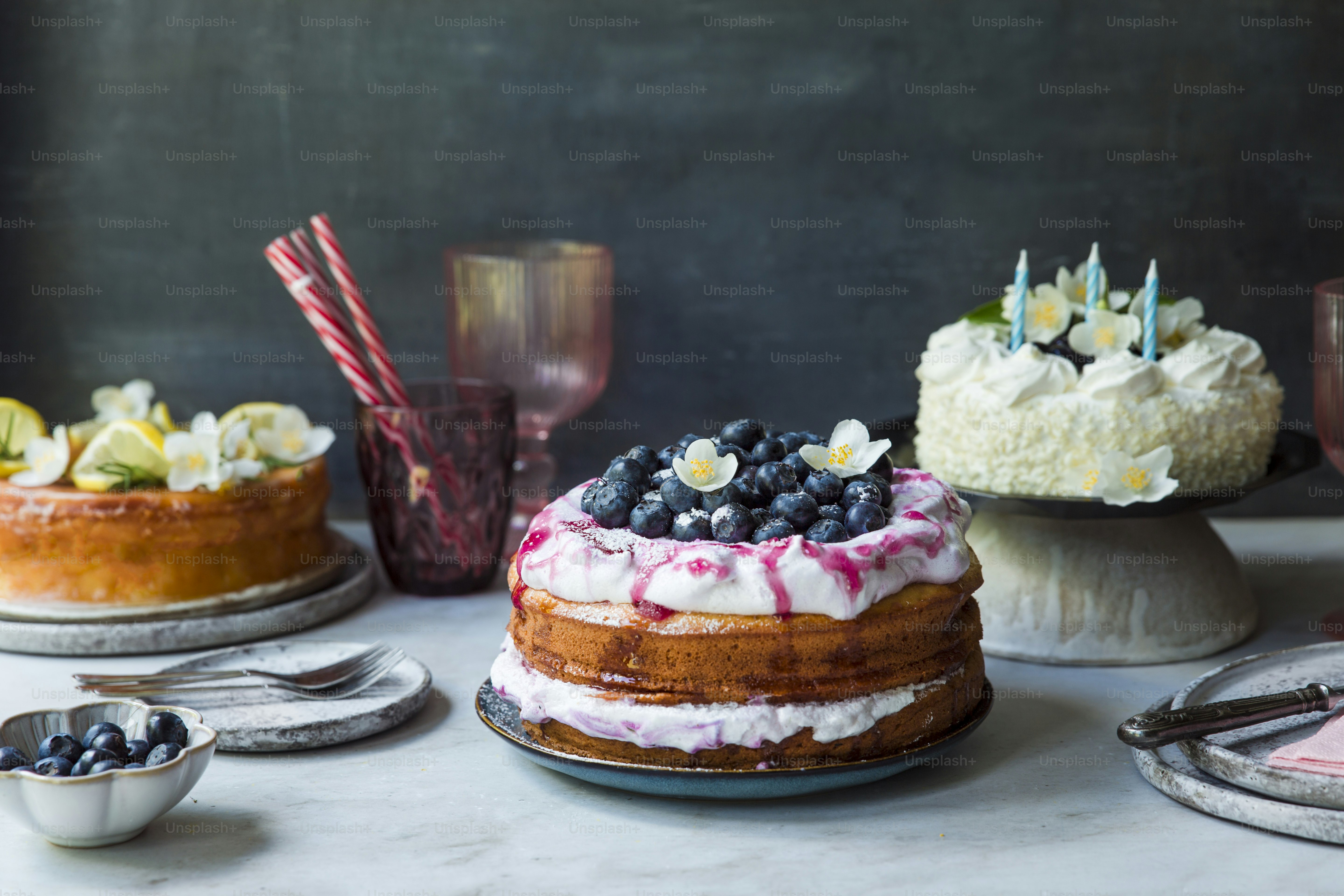 A table topped with cakes covered in frosting and blueberries photo ...
