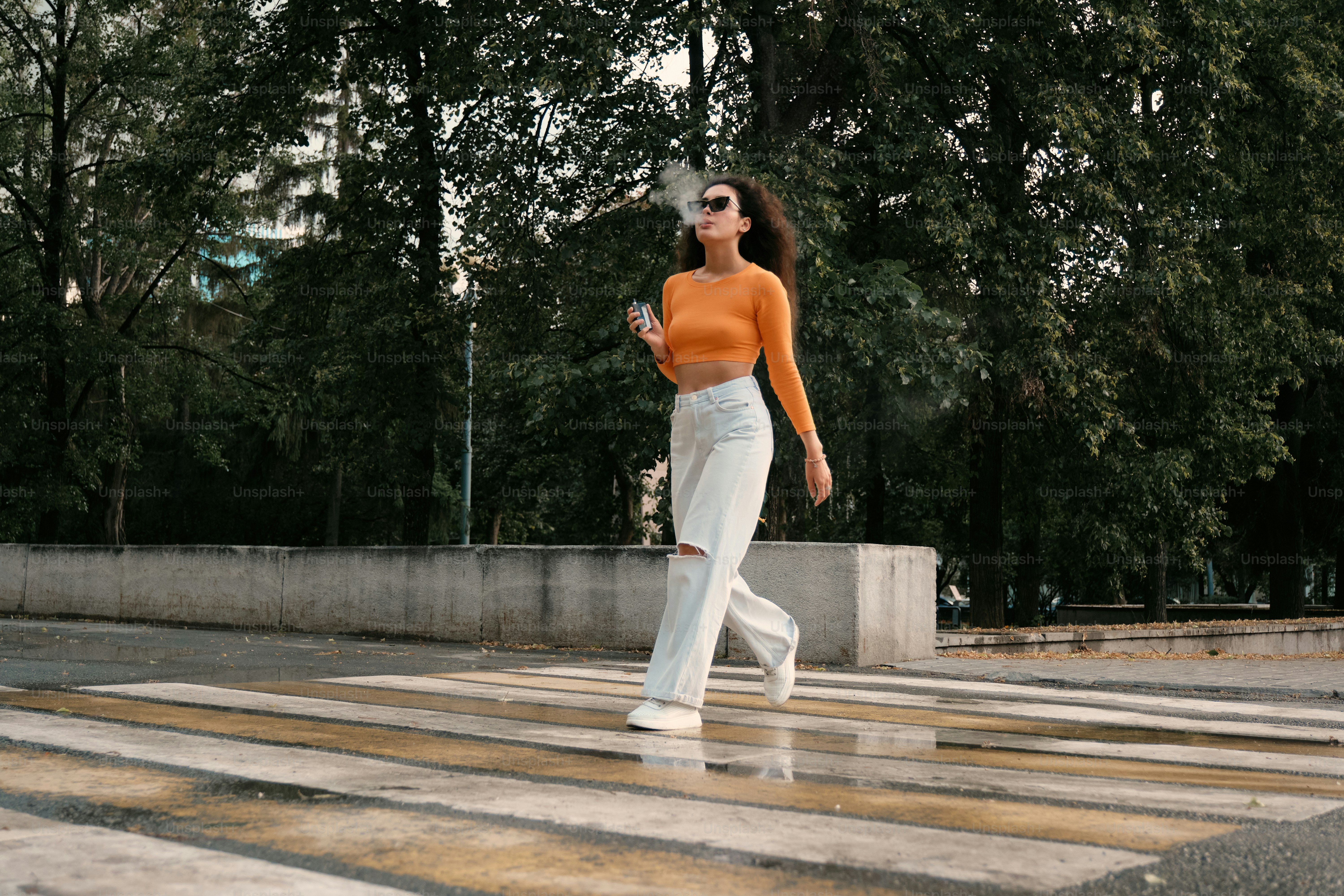 A woman walking across a cross walk in a park photo – Vaping Image on ...
