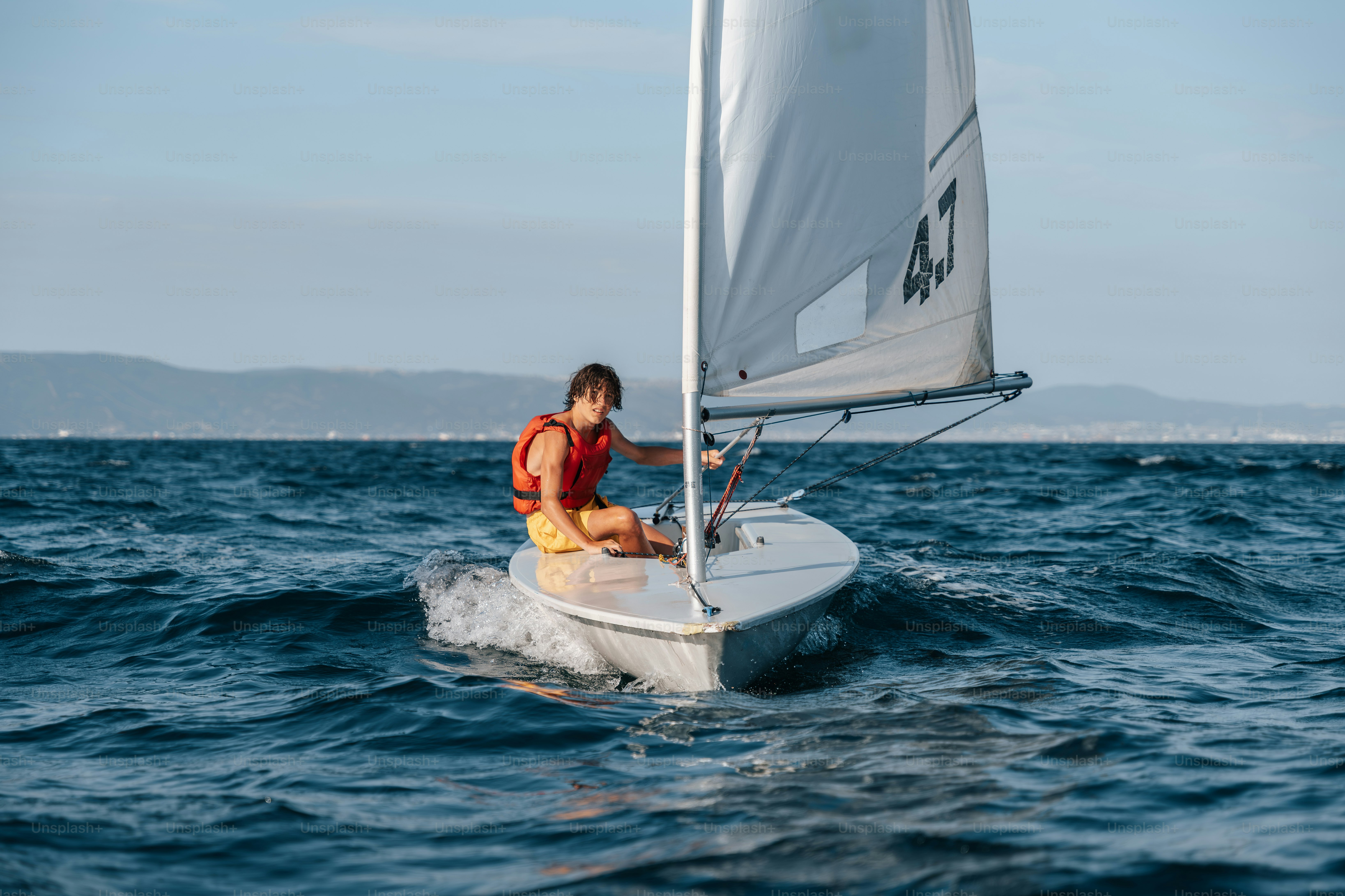 A man riding a sailboat on top of a body of water photo – Sailboat ...