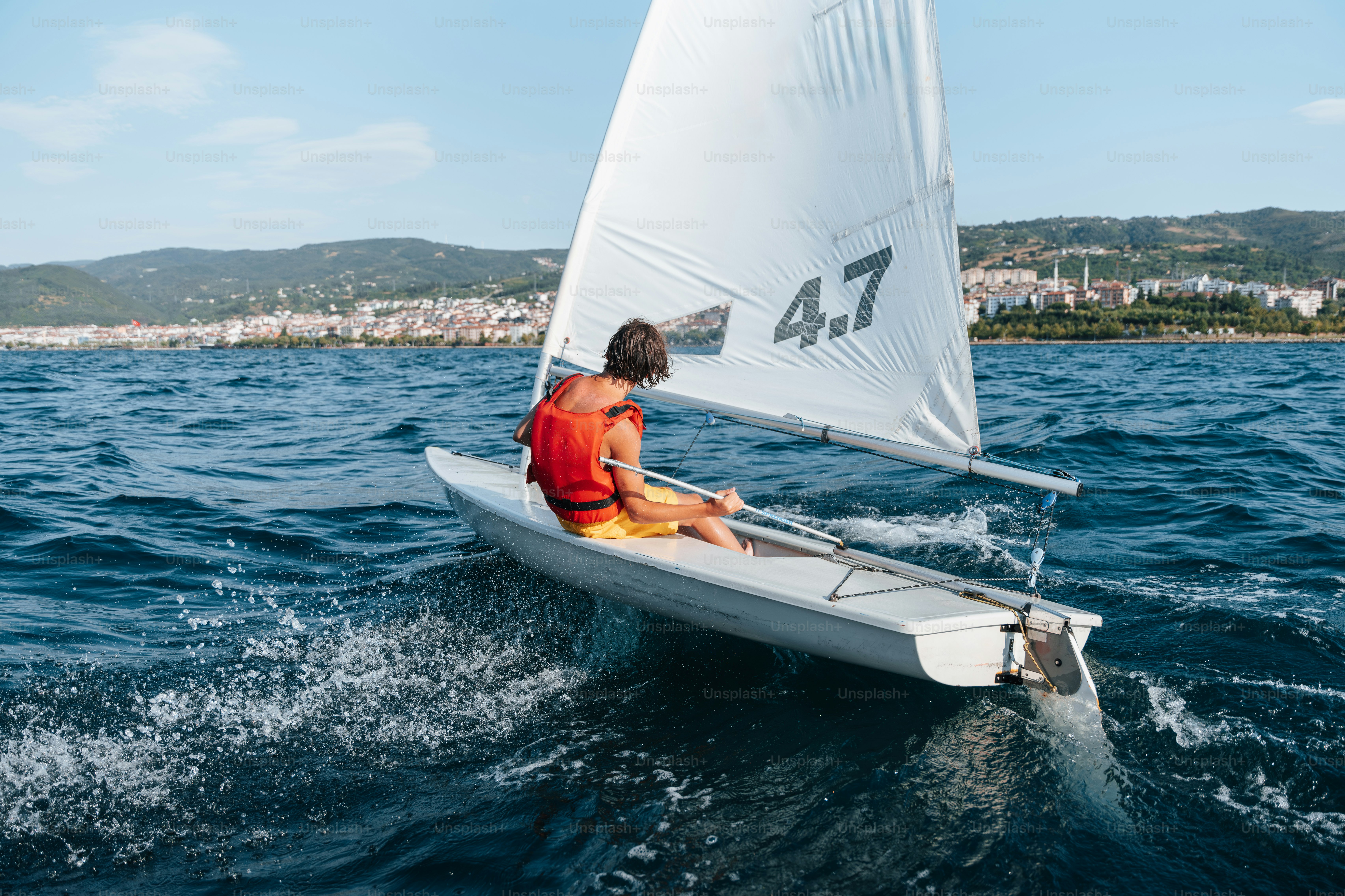 A man riding a sailboat on top of a body of water photo – Sailboat ...