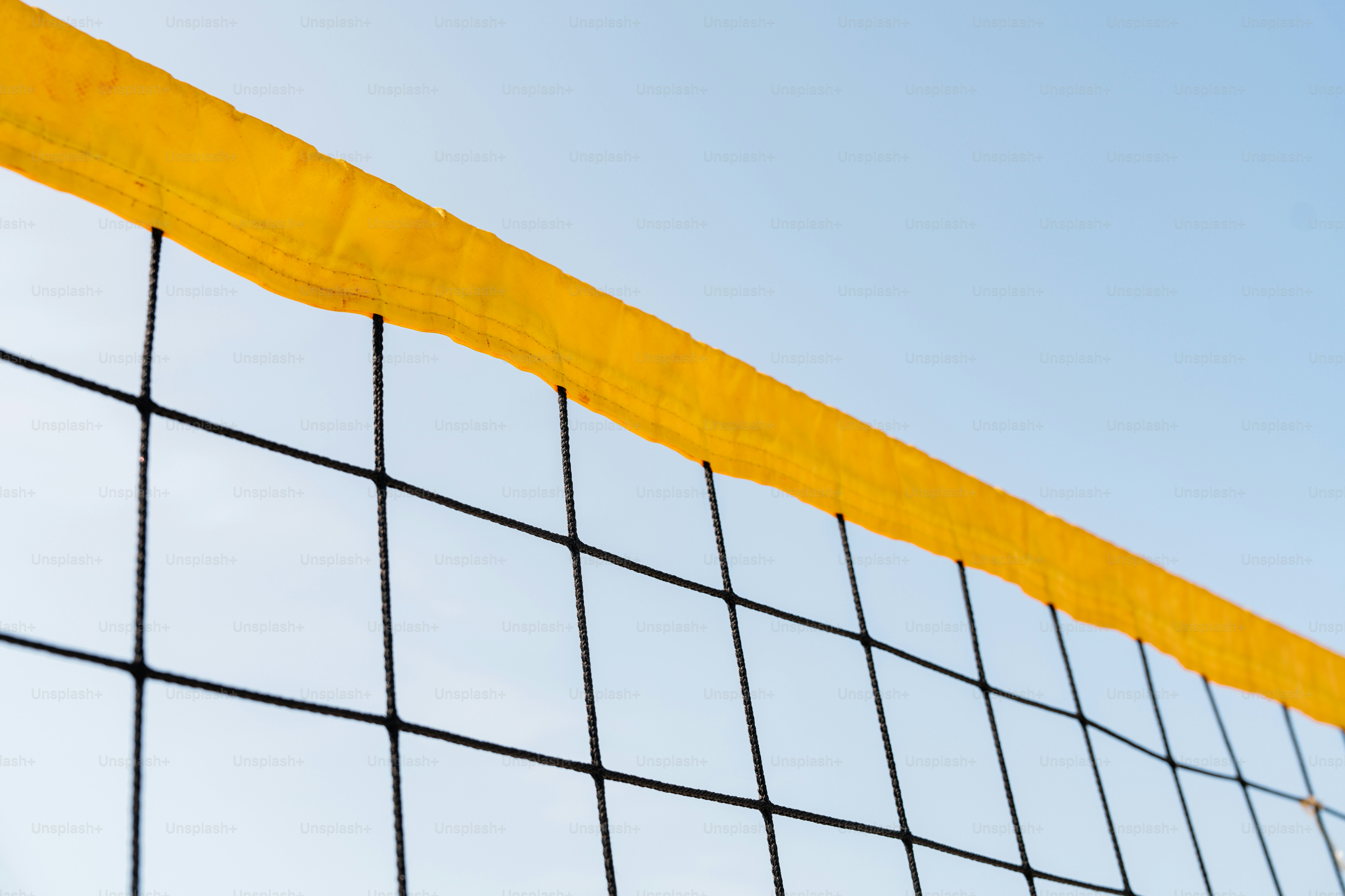 A close up of a yellow volleyball net with a blue sky in the background ...