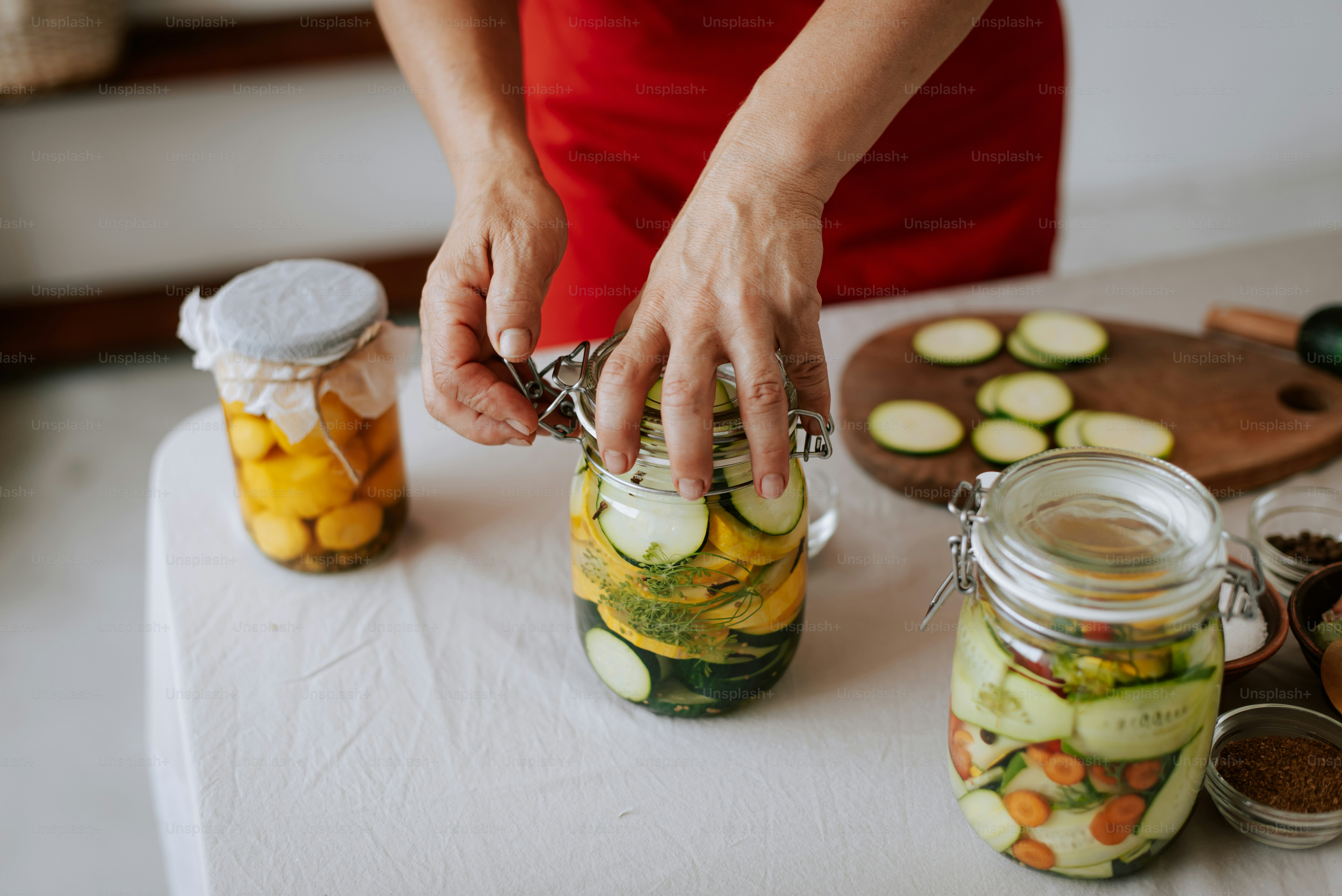 A woman is putting cucumbers in jars on a table photo – Preserving ...