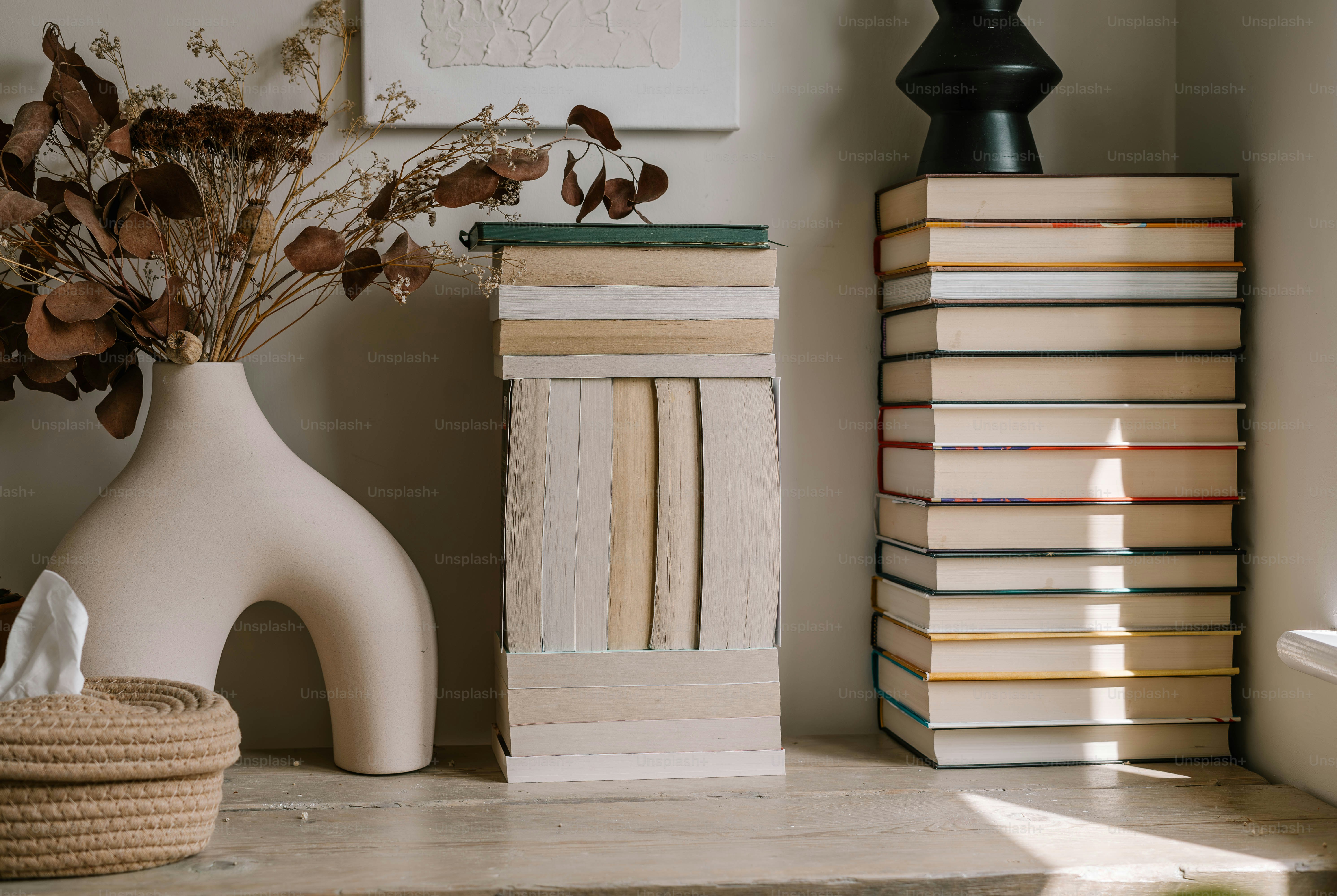 A stack of books sitting on top of a table next to a vase filled with ...