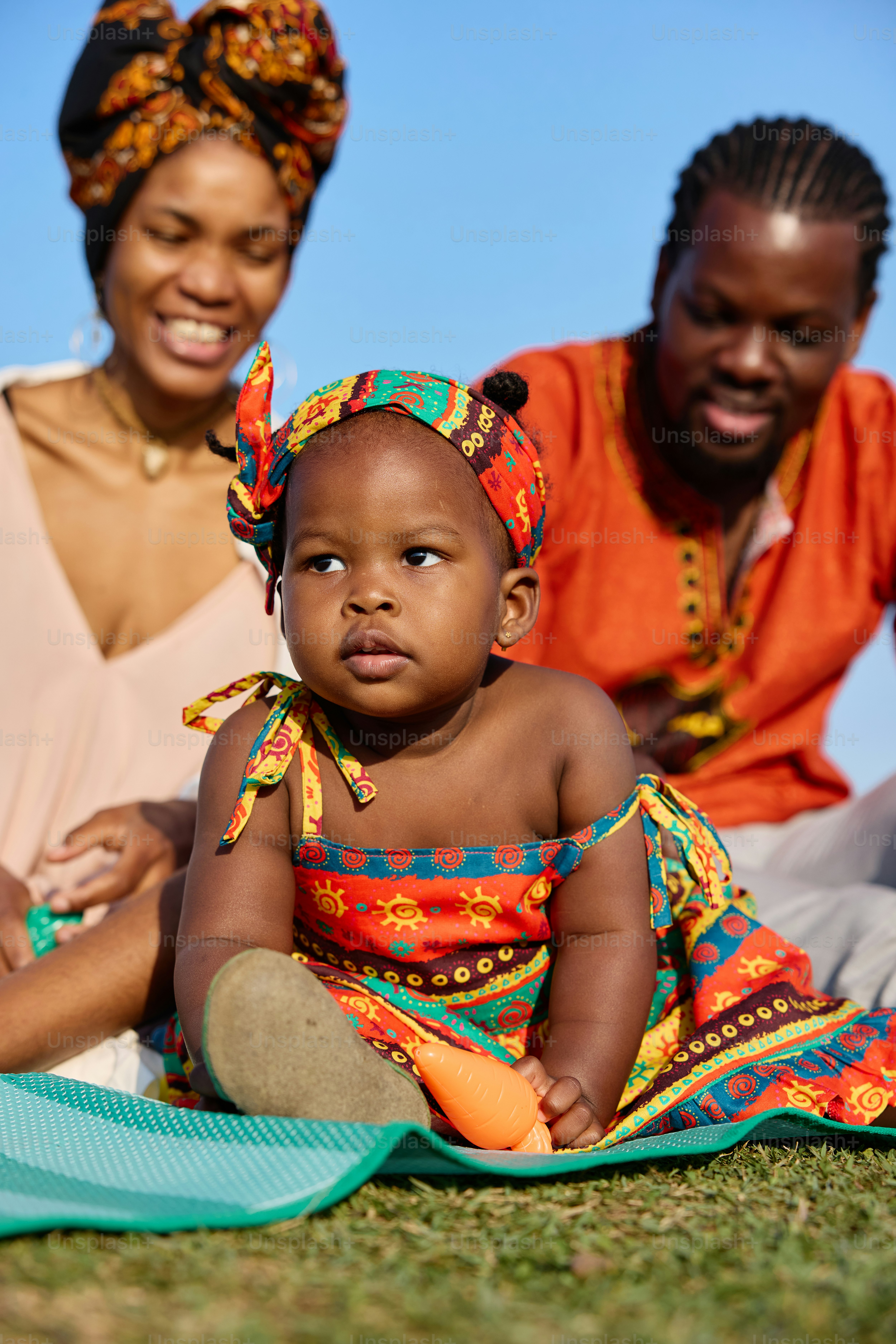 A baby sitting on the ground with two adults photo – Parenthood Image ...