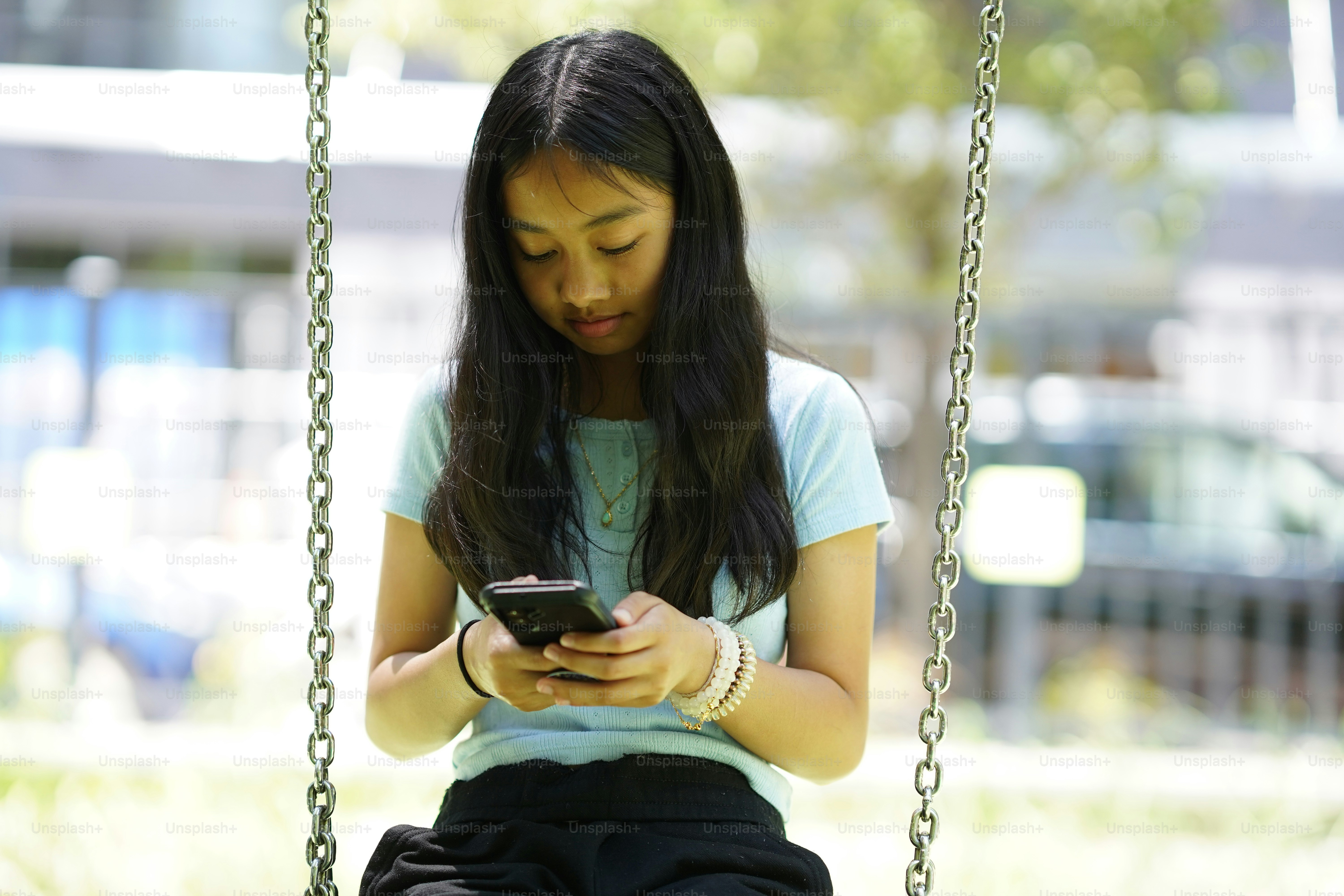 A woman sitting on a swing using a cell phone photo – Girl Image on ...