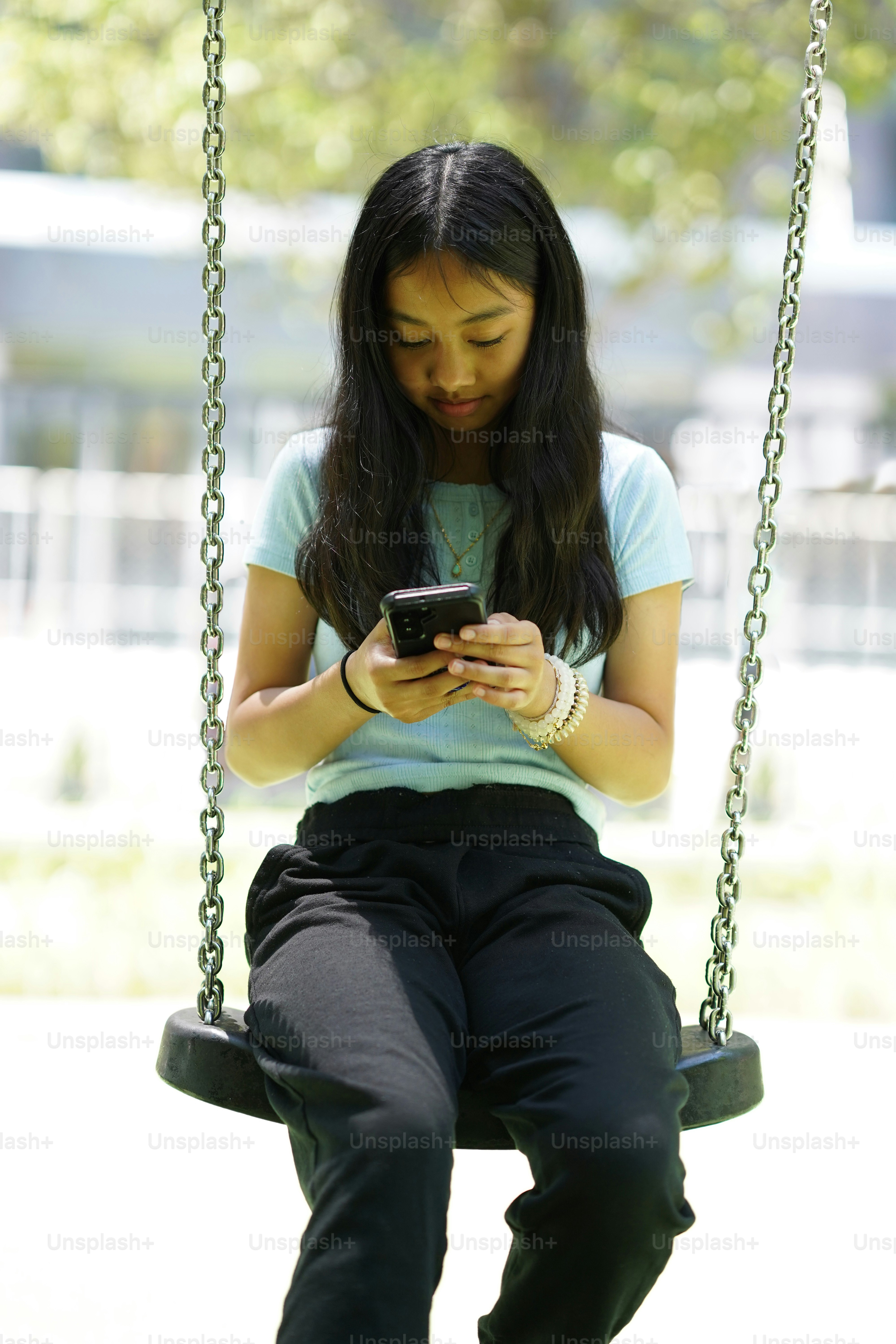 A woman sitting on a swing using a cell phone photo – Children Image on ...