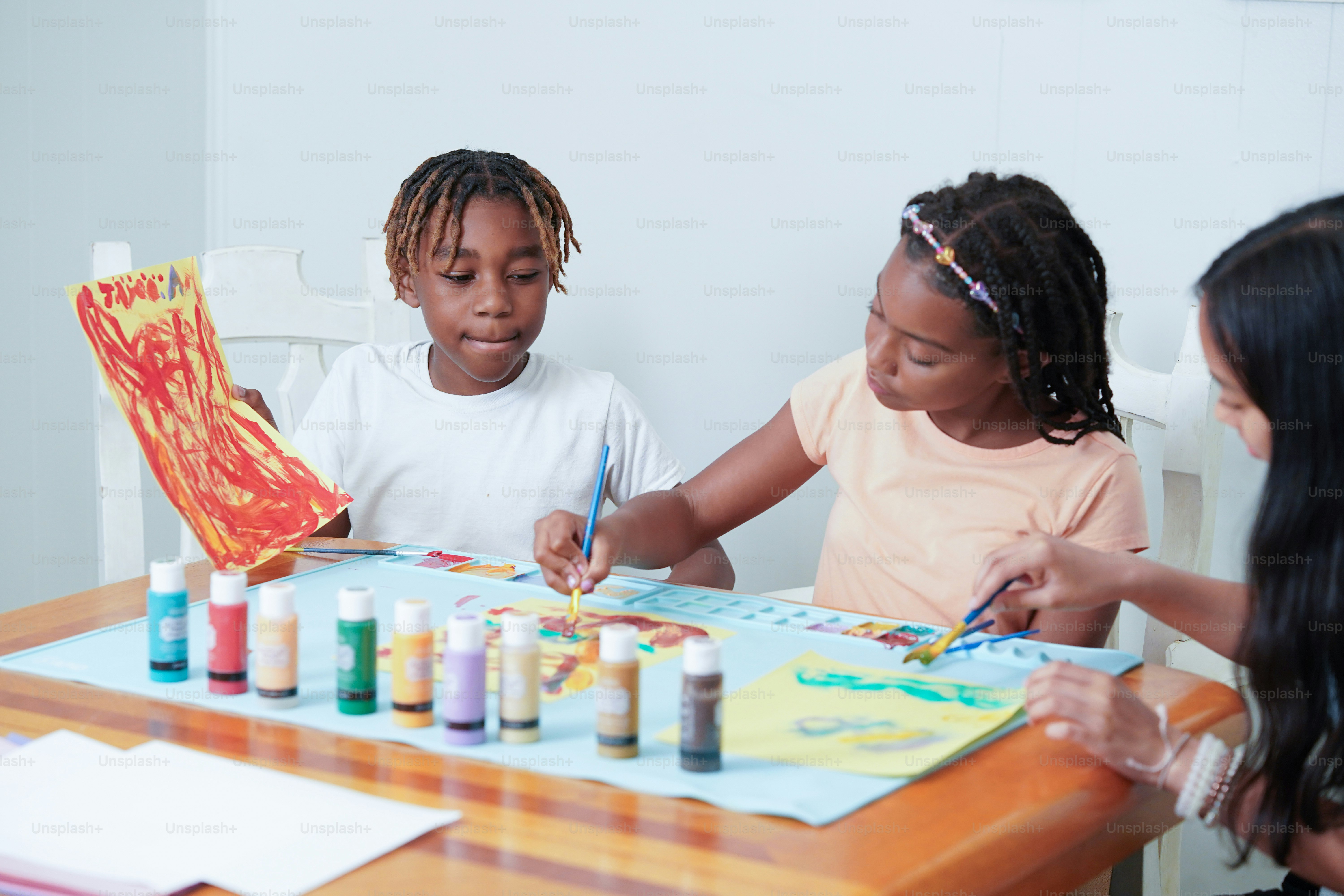 A group of children sitting around a table with paint photo – Gen alpha ...