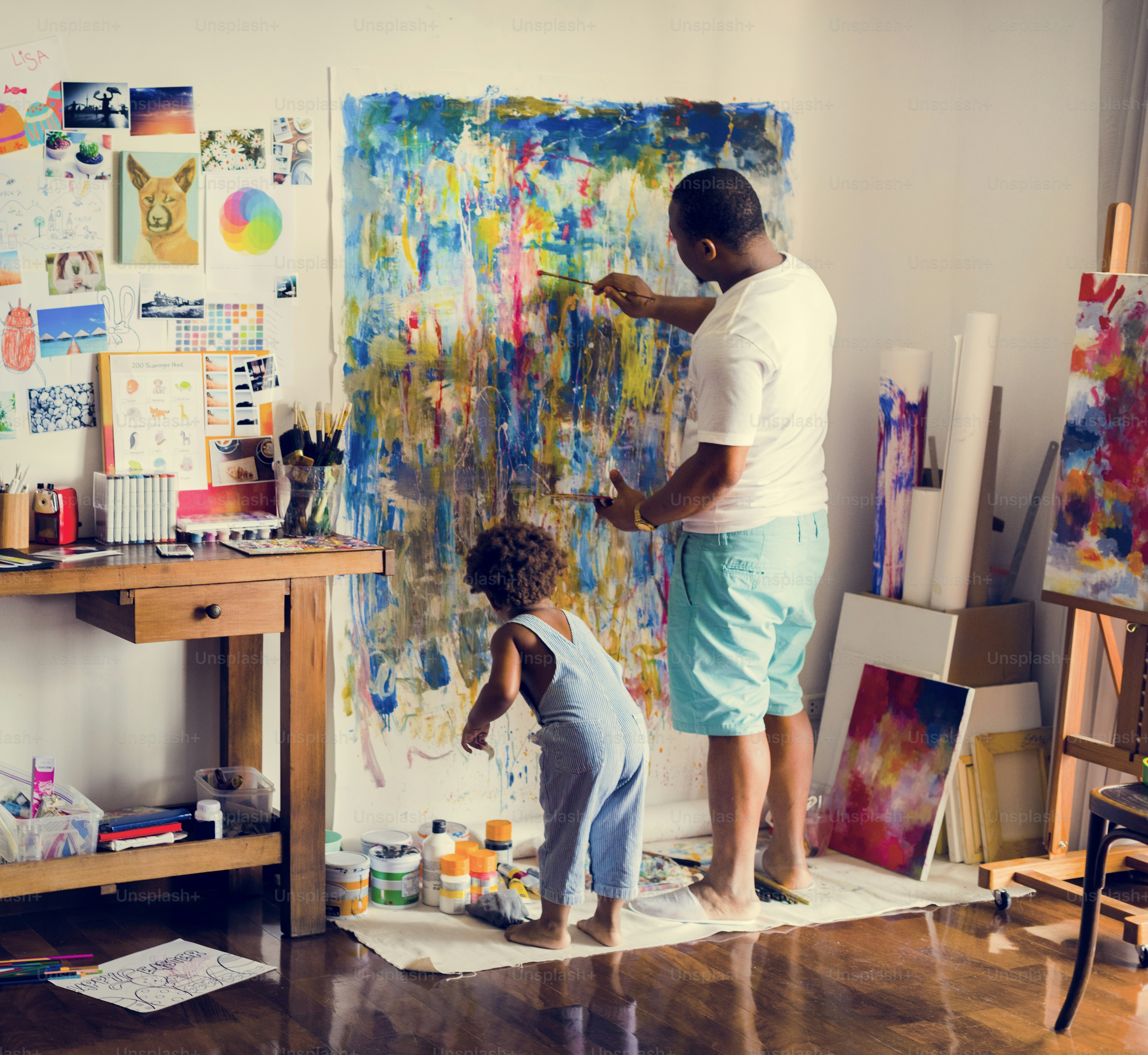 Black artist dad doing his art work with his child sitting nearby ...
