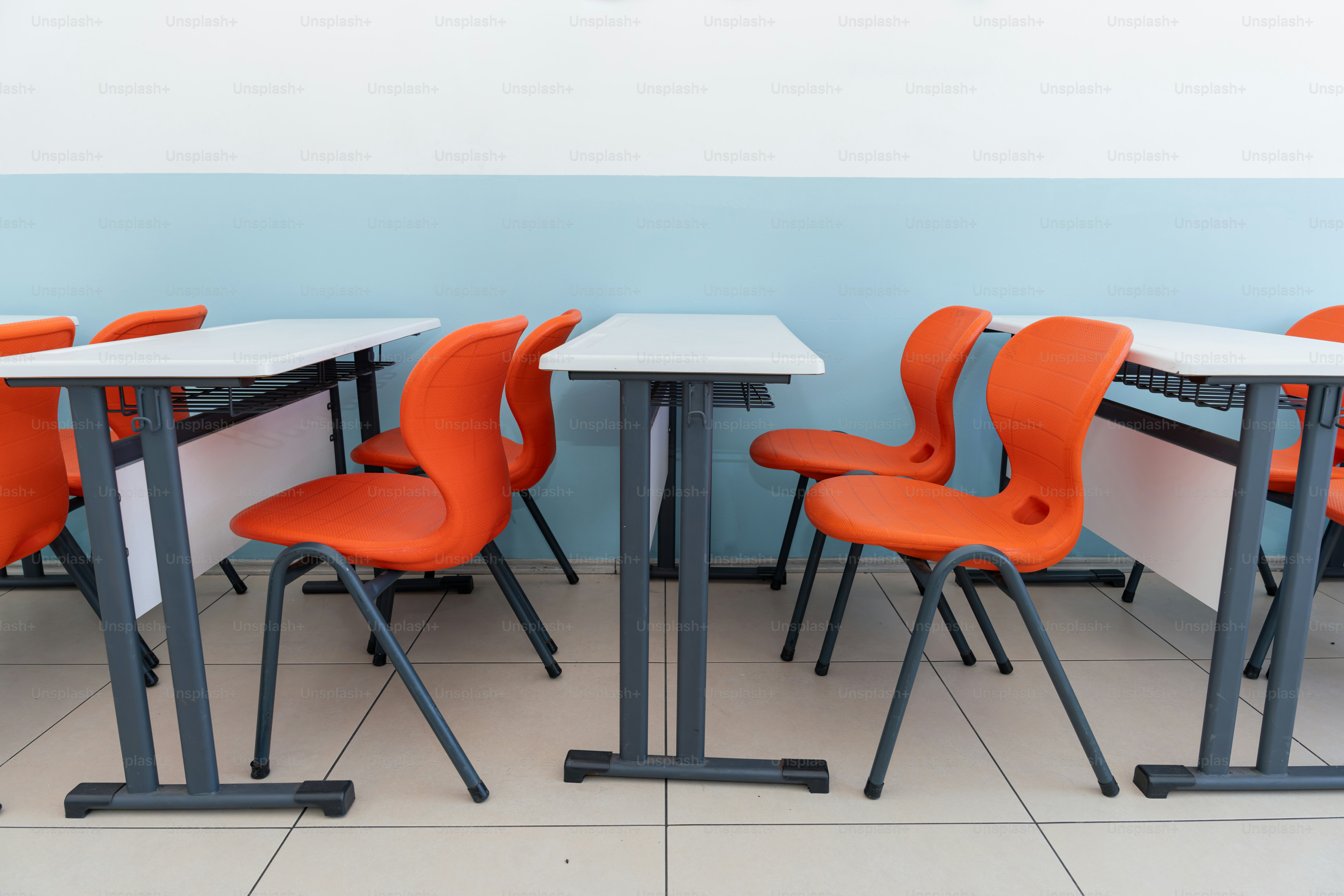 A group of desks with orange chairs in a room photo – School Image on ...