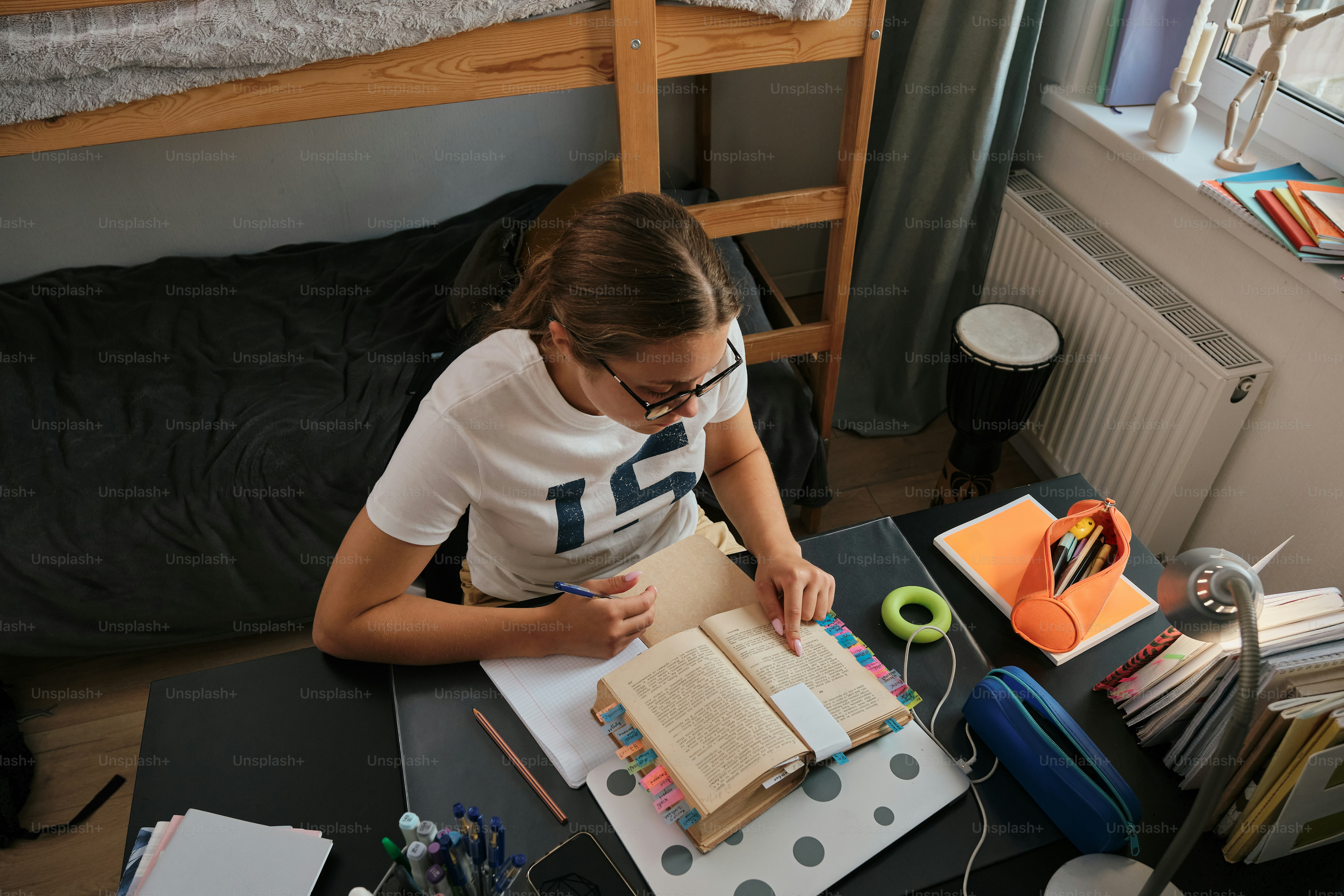 A person sitting at a desk writing in a book photo – Student Image on ...