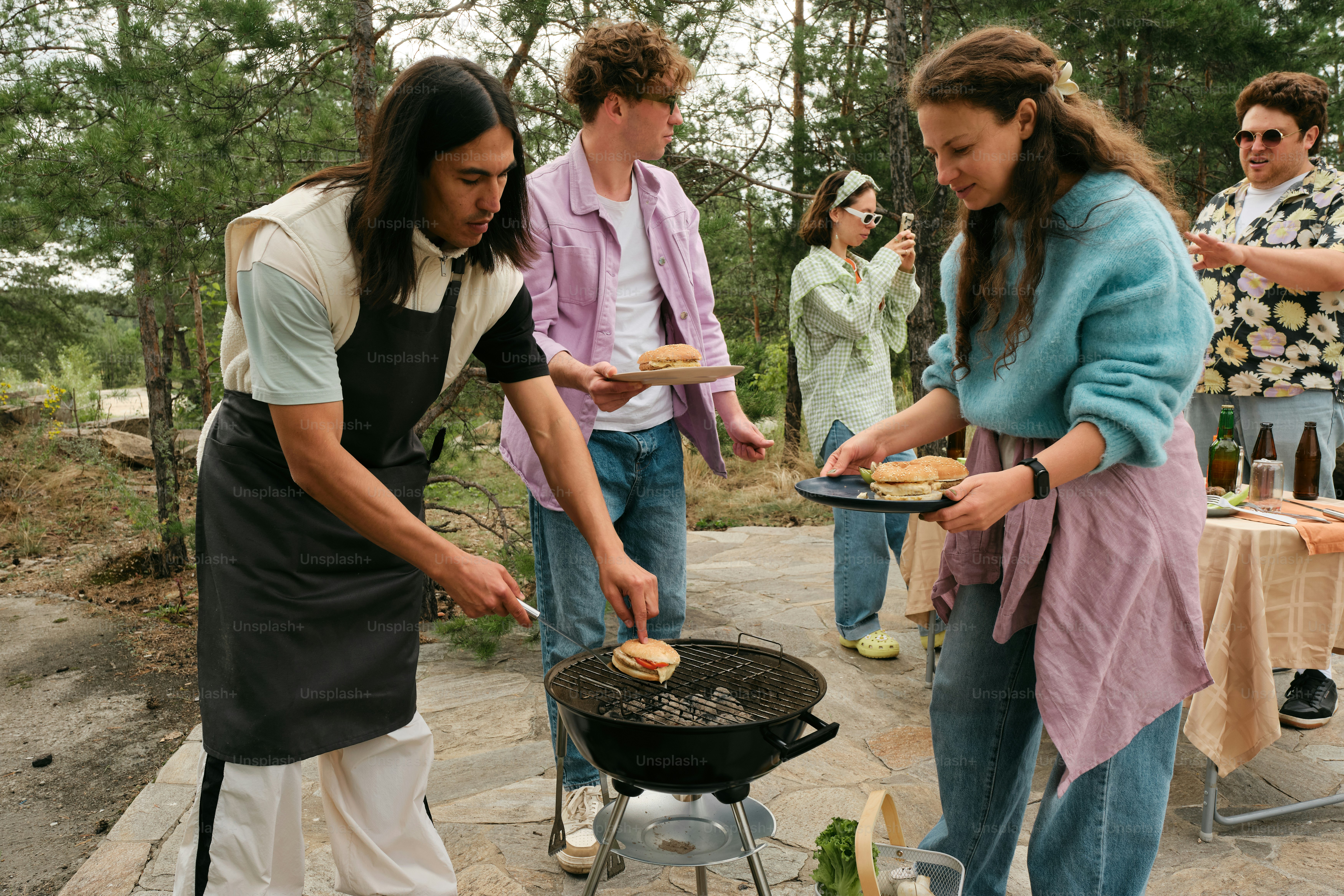 A group of people standing around a grill with food on it photo ...