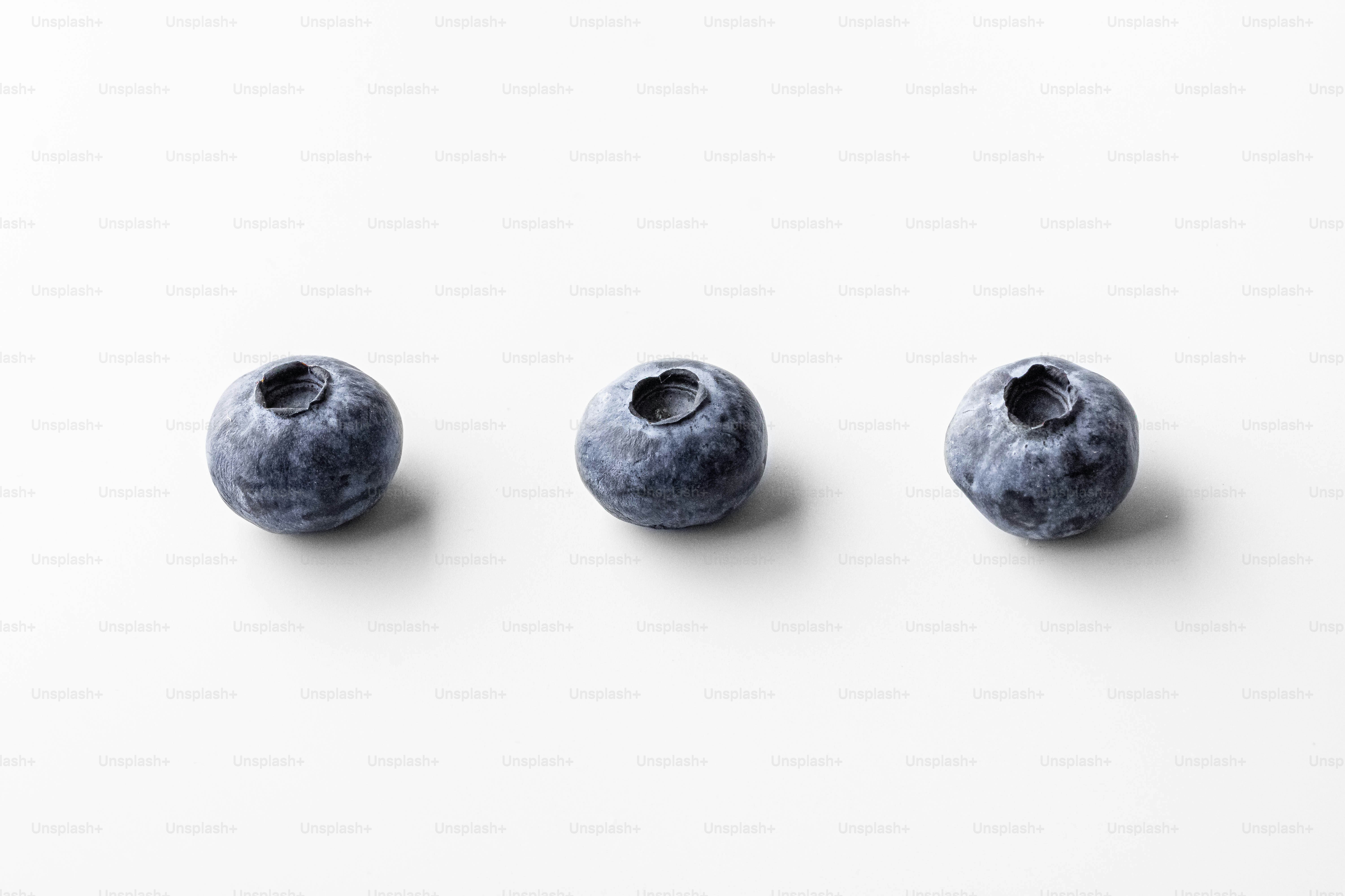 Three blueberries sitting in a row on a white surface photo – Blueberry ...