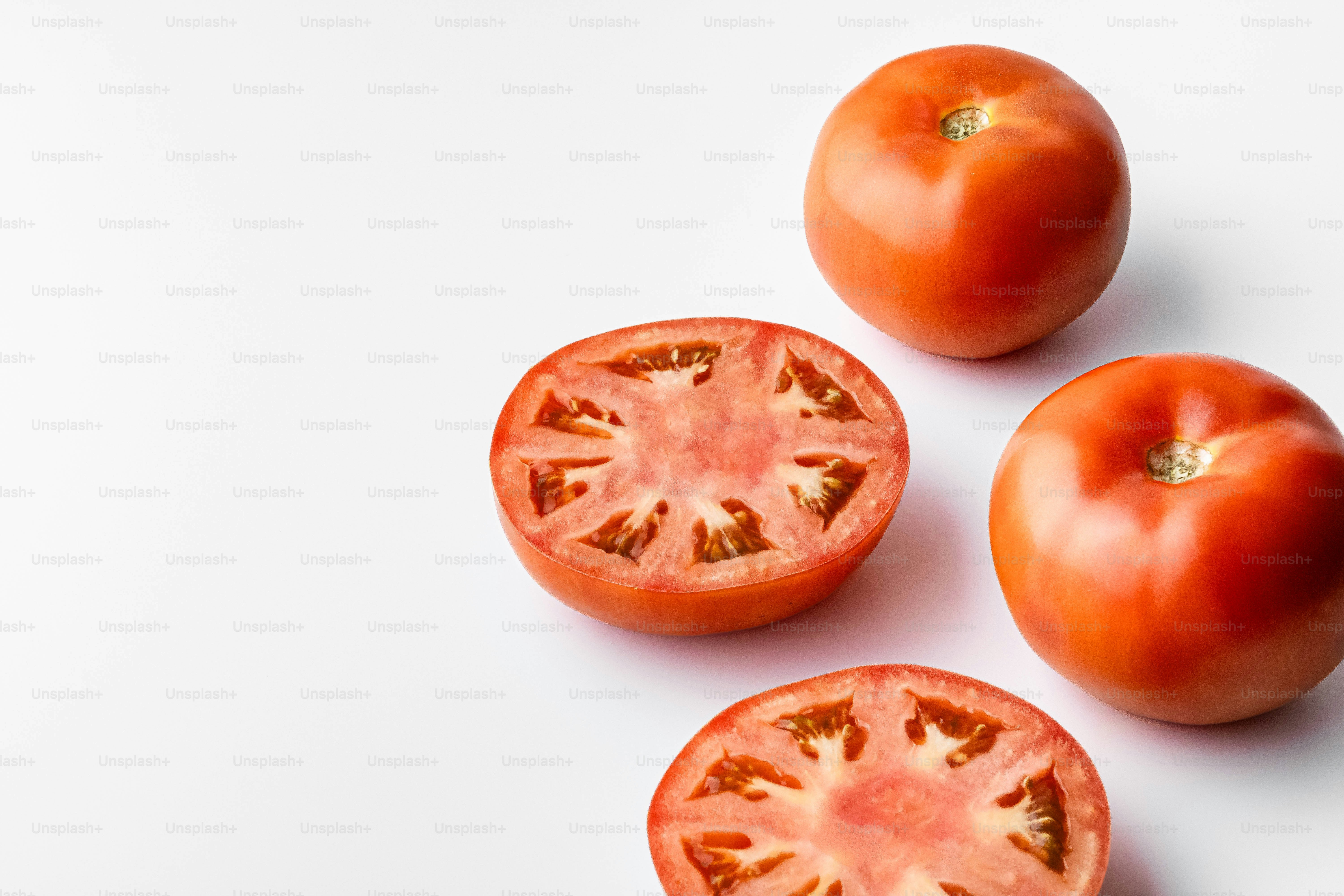 Three tomatoes cut in half on a white surface photo – Tomato Image on ...