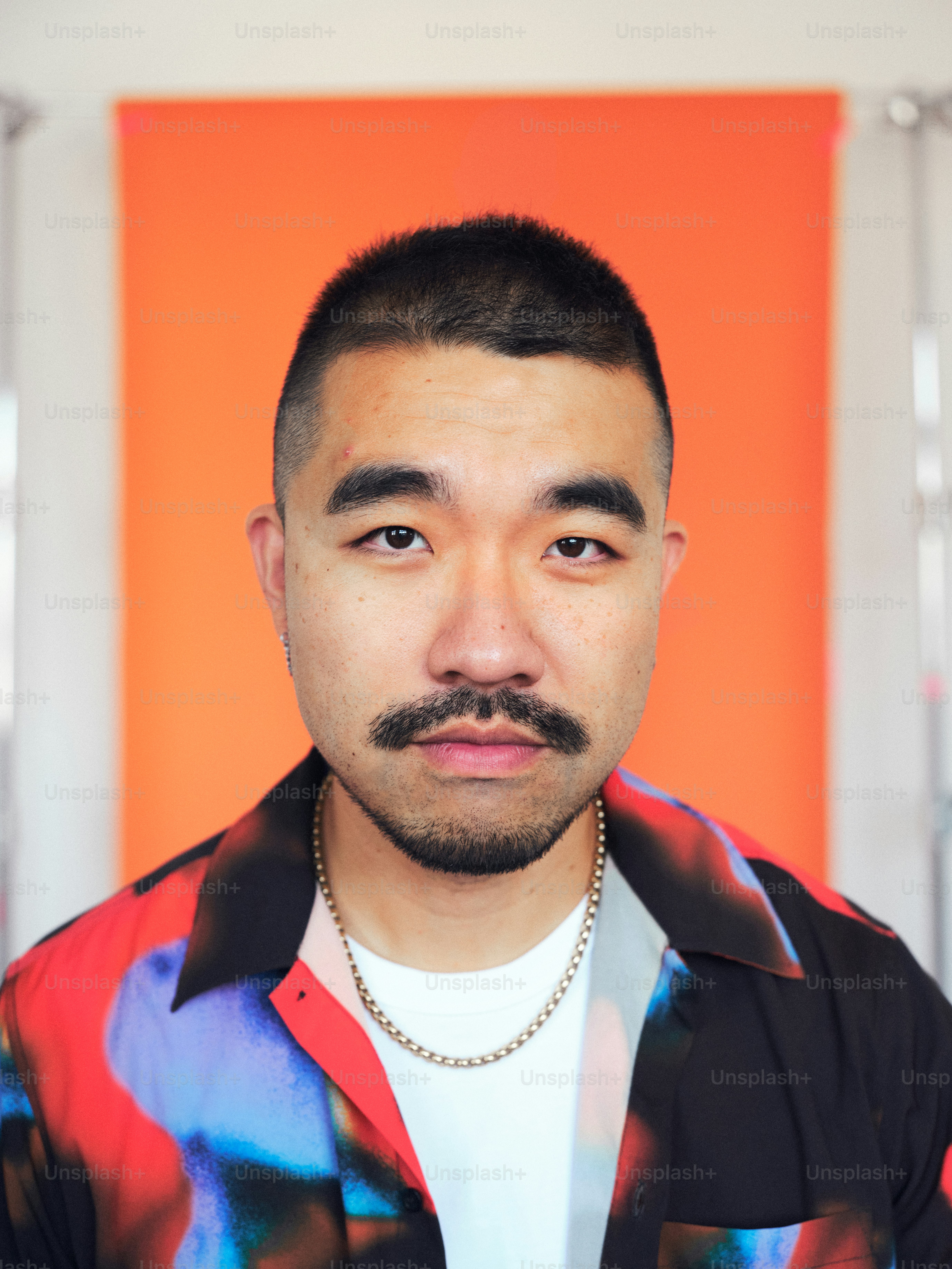 A man with a moustache standing in front of an orange wall photo ...