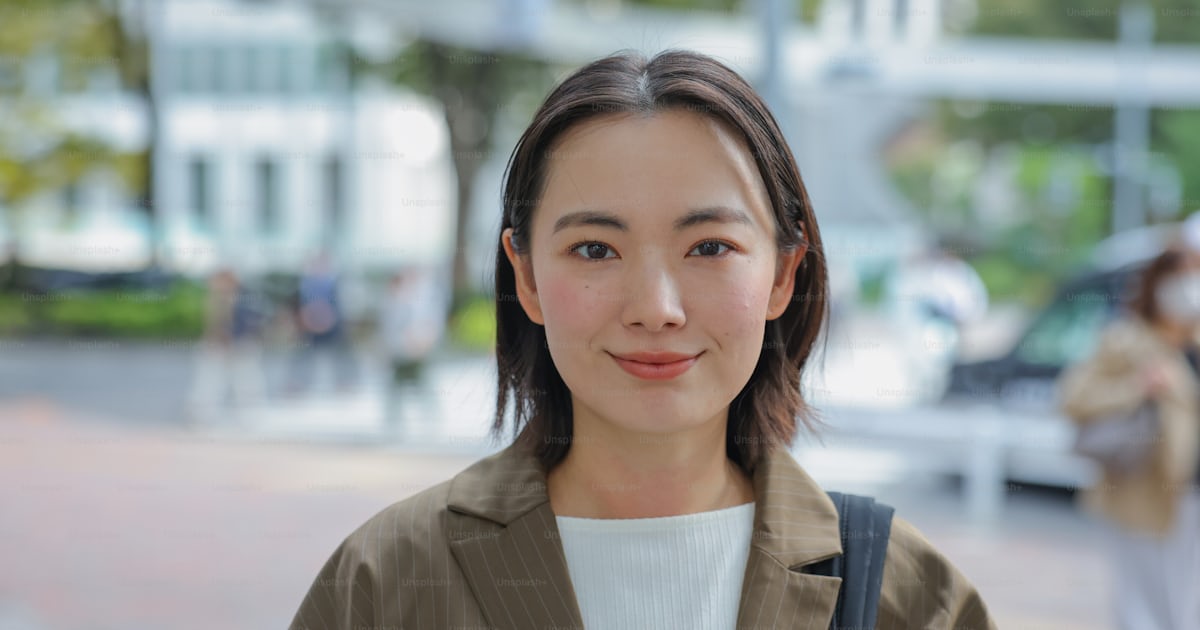 屋外でカメラを見ているアジアのビジネスウーマン、朝の通勤中の若い女性。 明るい表情で楽しそうに仕事に向かう女性。の写真 Unsplashの