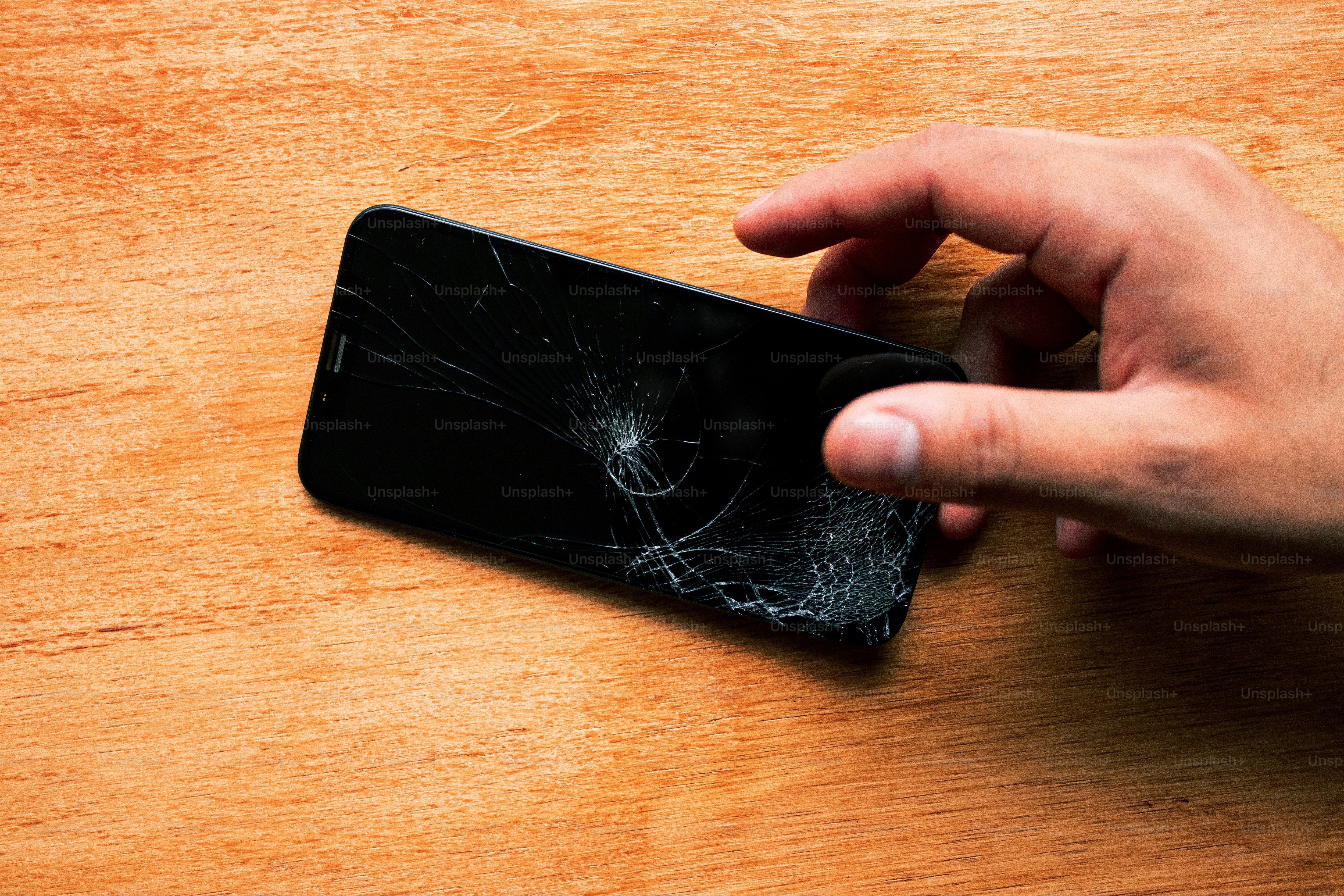 A hand holding a broken cell phone on top of a wooden table photo ...