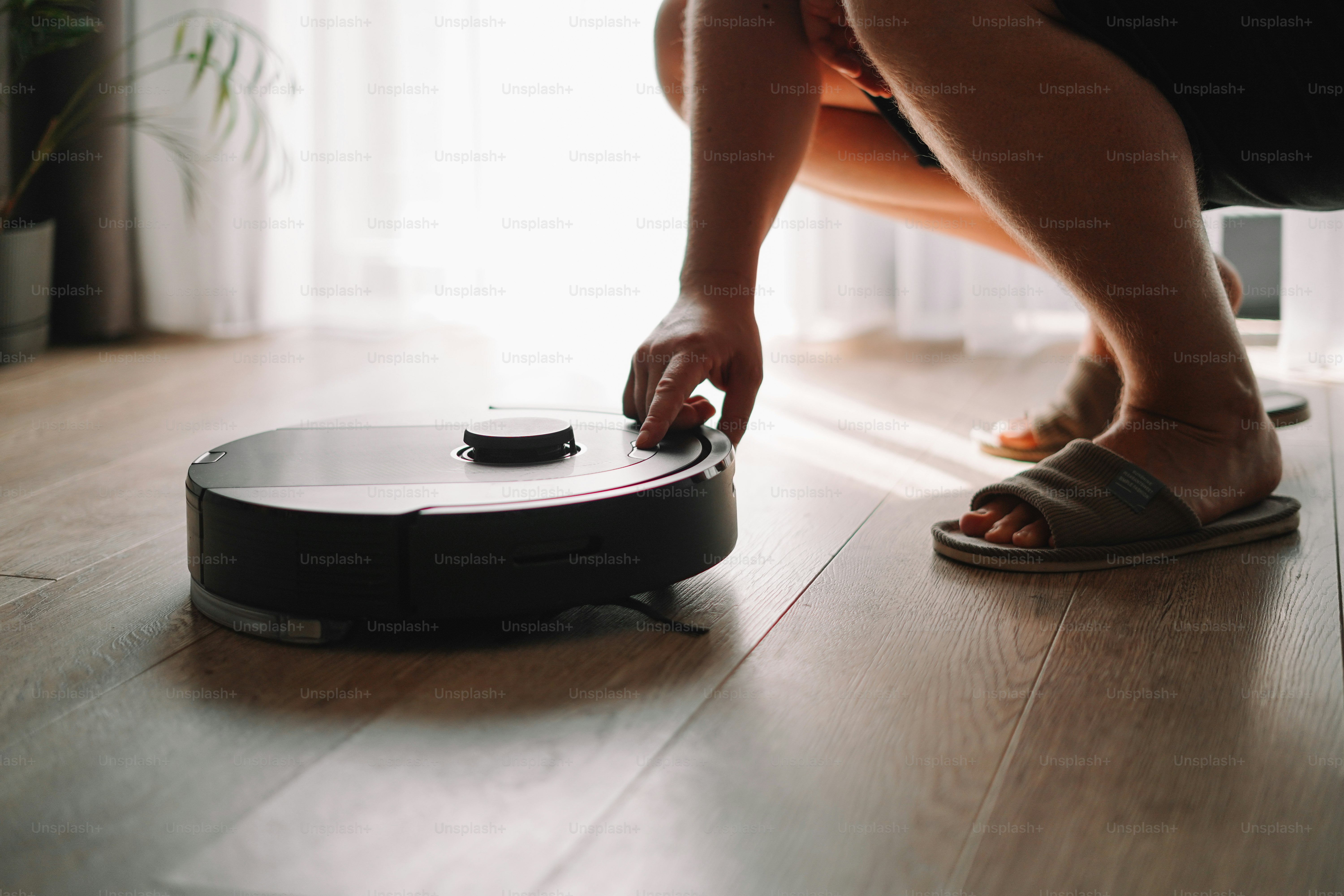 A woman kneeling on the floor next to a robotic vacuum photo – Smart ...