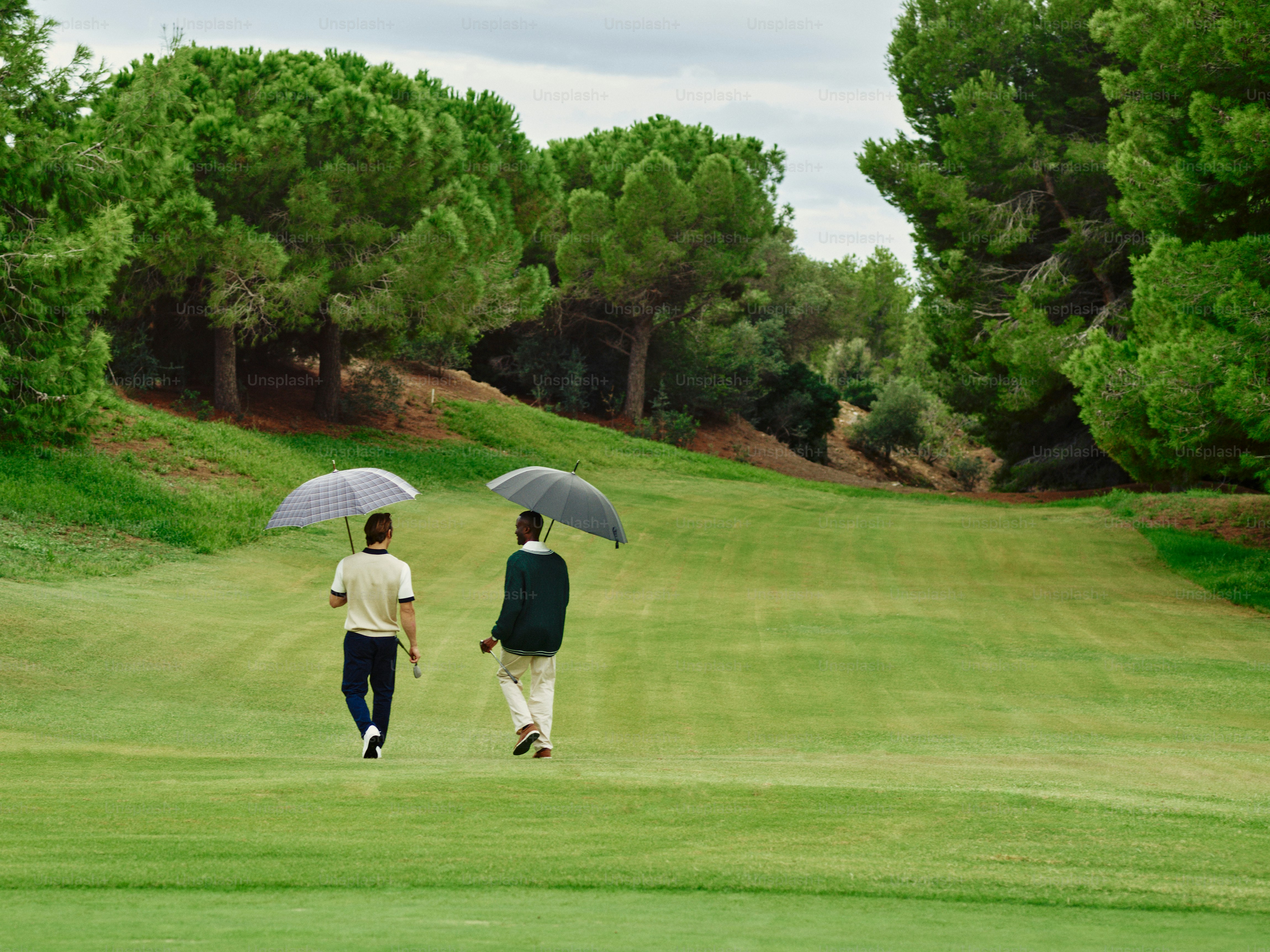 Two men walking on a golf course holding umbrellas photo – Green Image ...